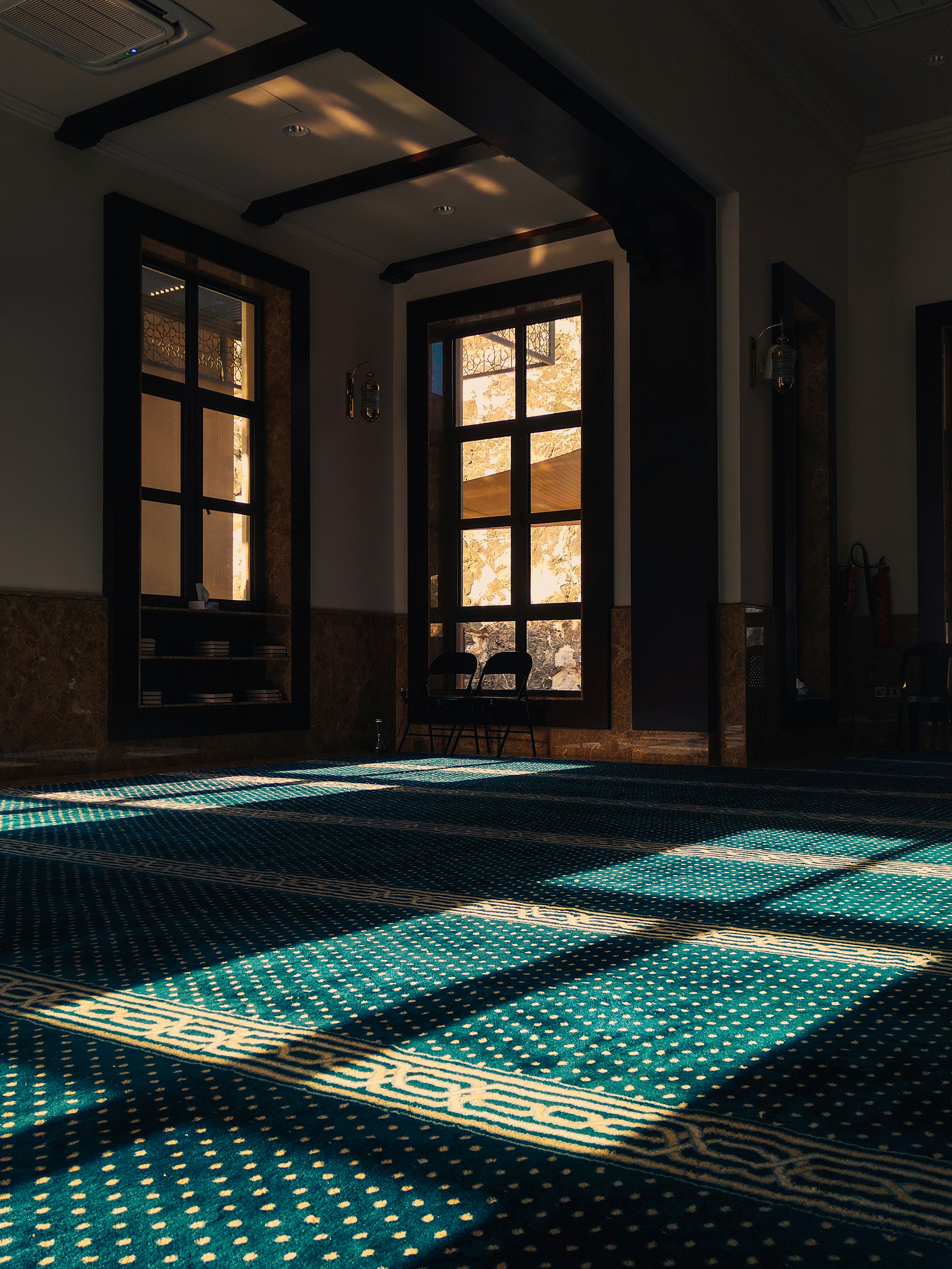 Sunlight streams through windows onto a mosque's carpet.