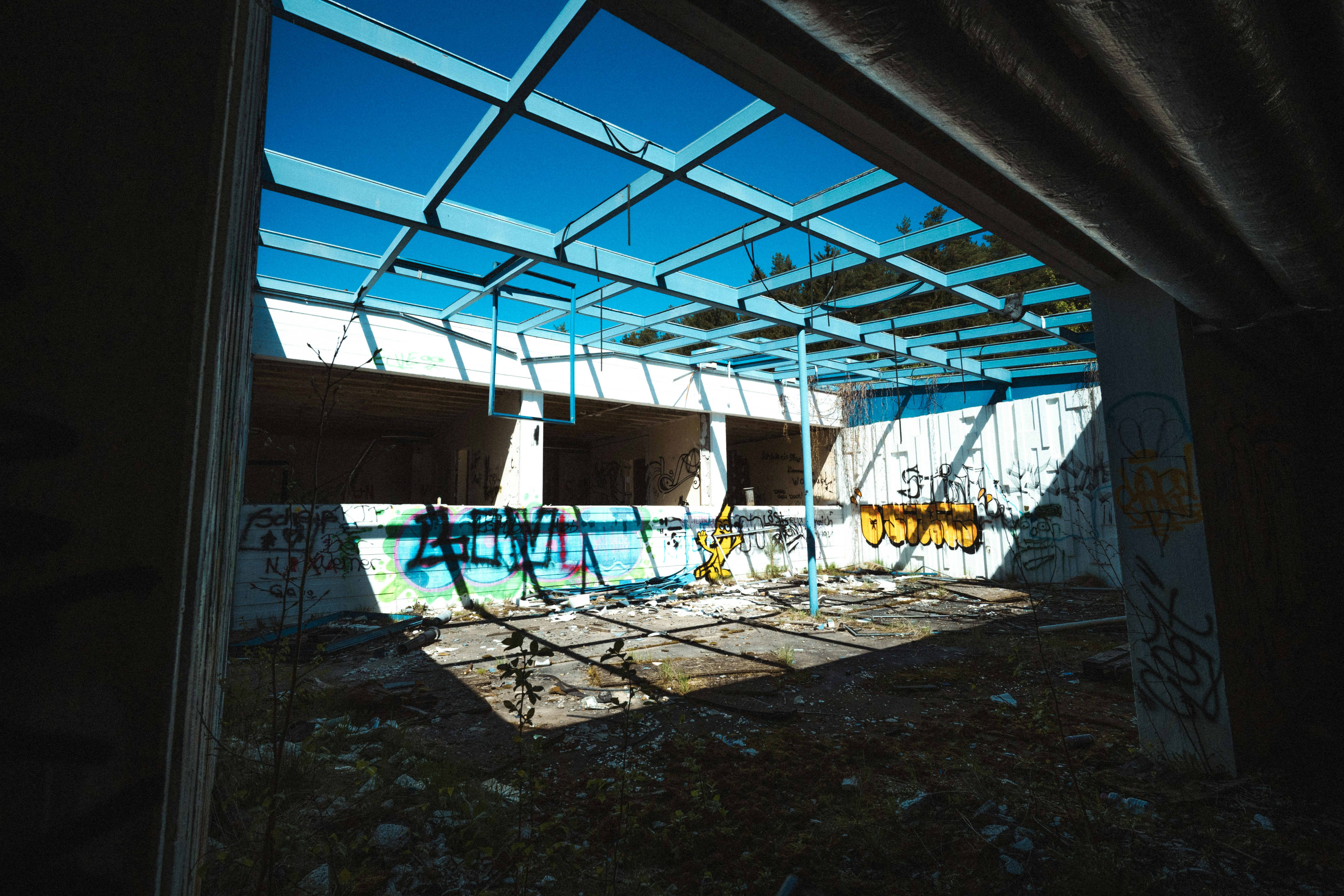 Graffiti-covered walls and a partially collapsed ceiling create a haunting atmosphere in an abandoned structure. Sunlight filters through, illuminating the remnants of a once vibrant space.