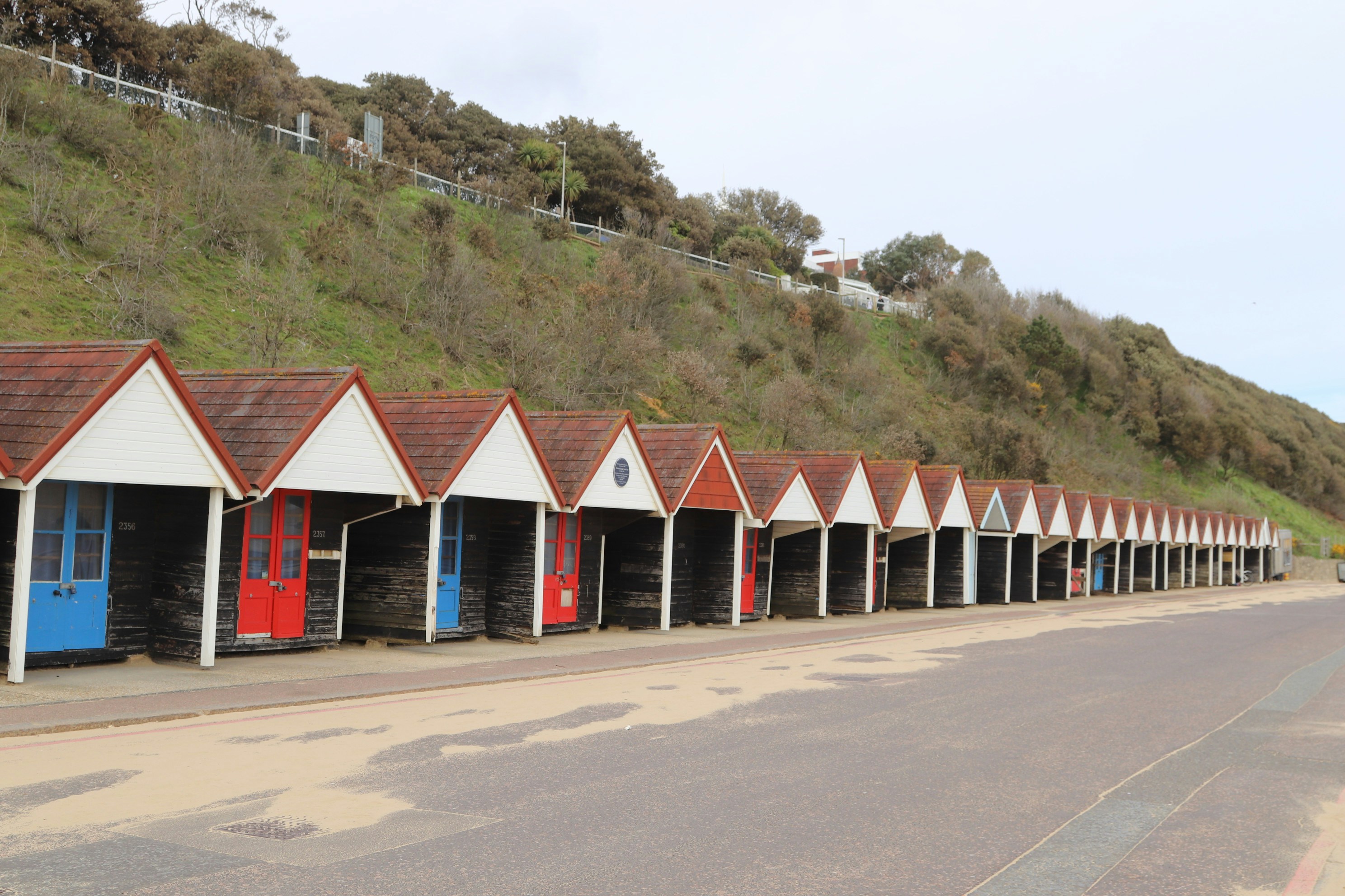 Red Roofed Row: A-Frame Beach Huts Align Along a Wind-Swept Esplanade