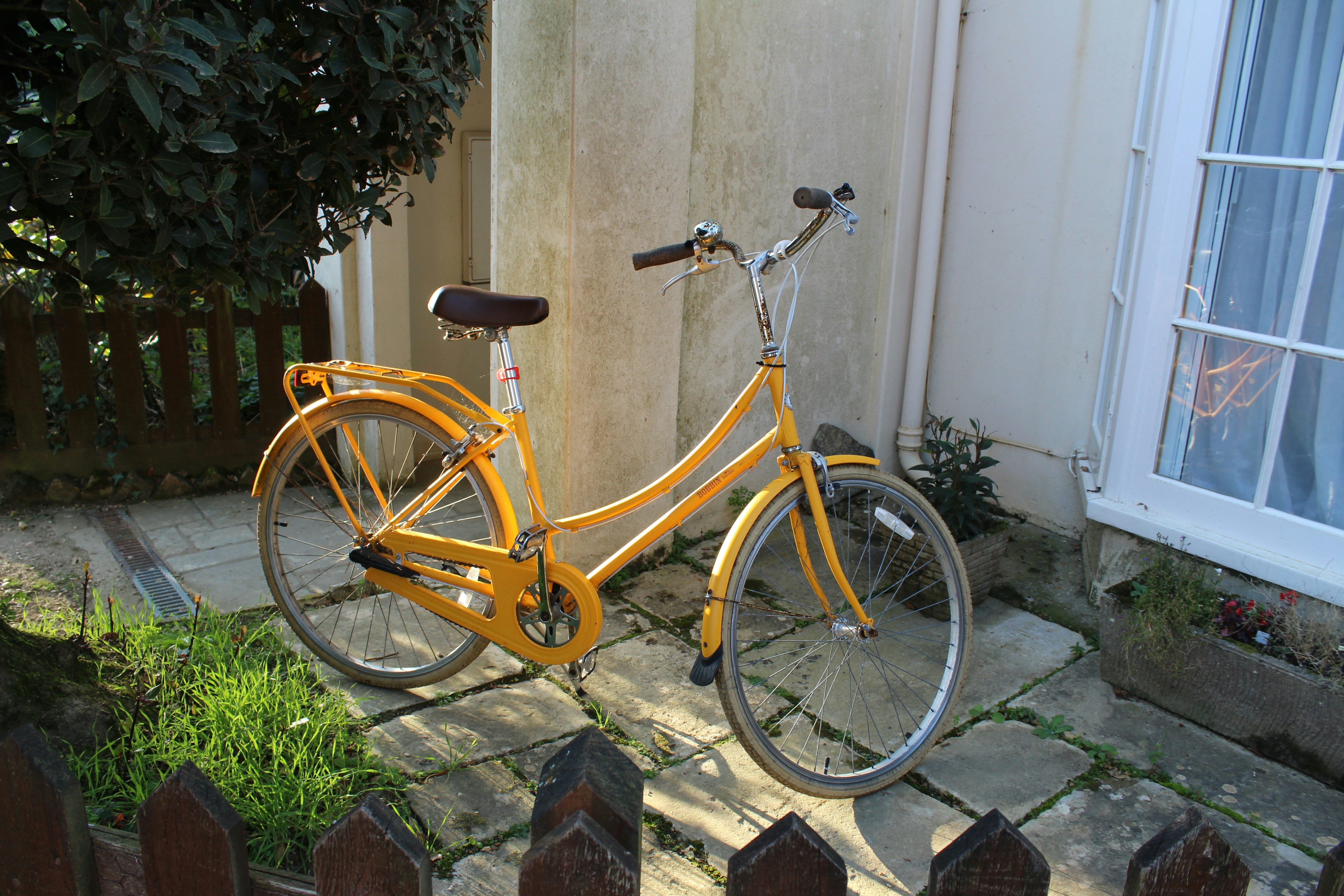 Sunlit Yellow Bicycle Framed by a Picket Fence in a Cottage Courtyard
