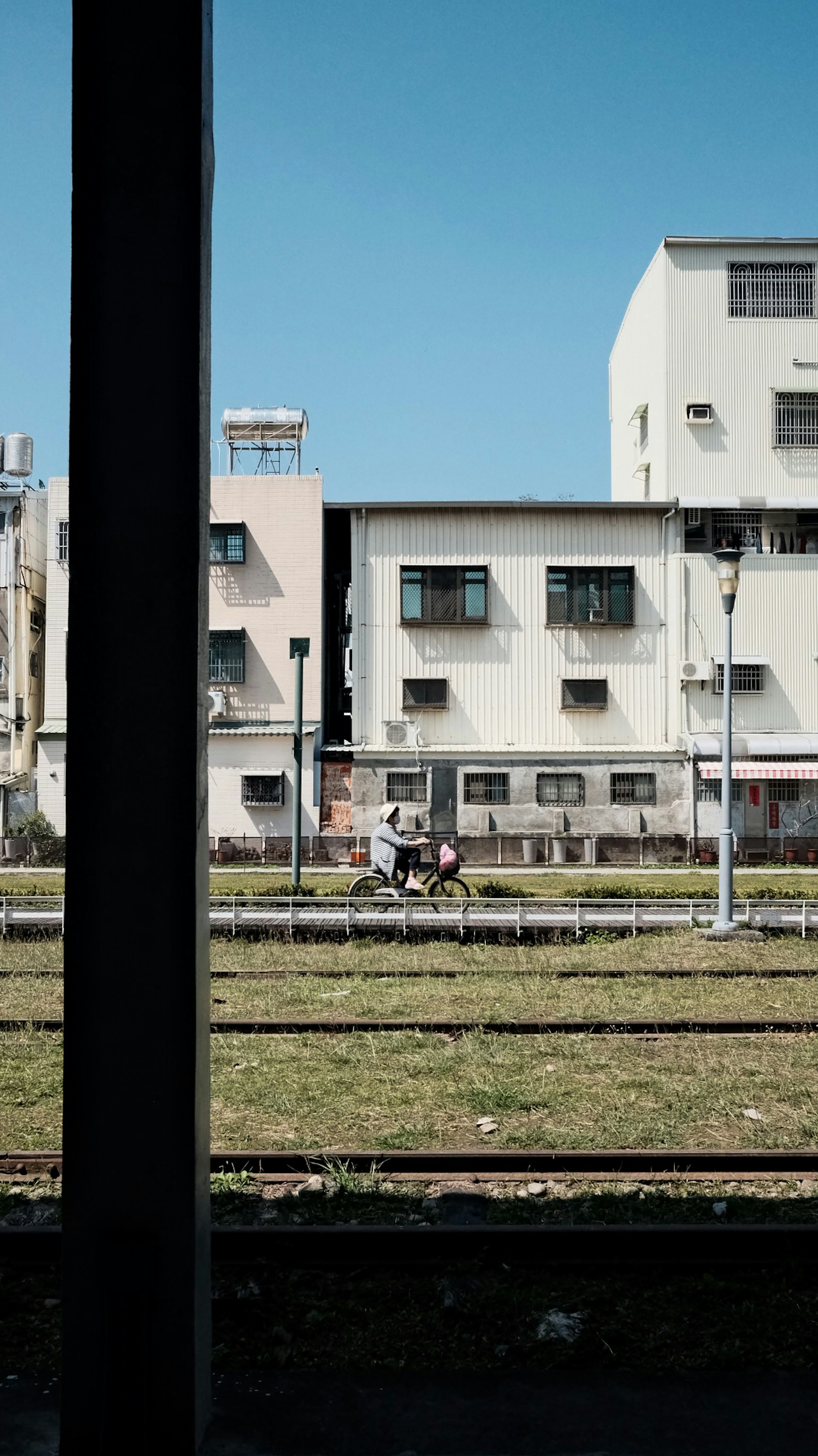 Two cyclists glide along sunlit rails before a pale industrial façade