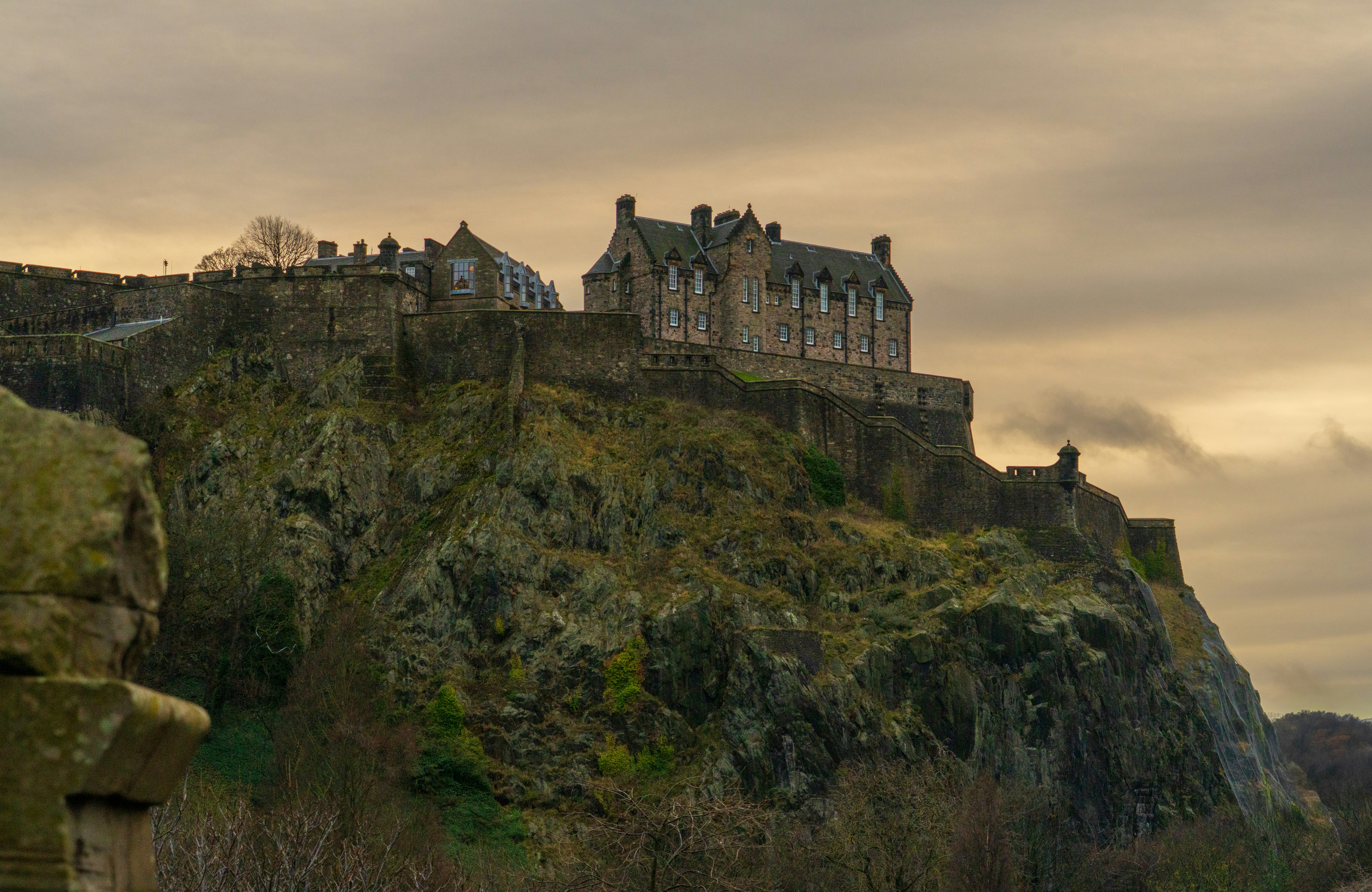 Historic castle perched atop a rocky cliff under a moody sky, showcasing architectural grandeur against a dramatic backdrop.