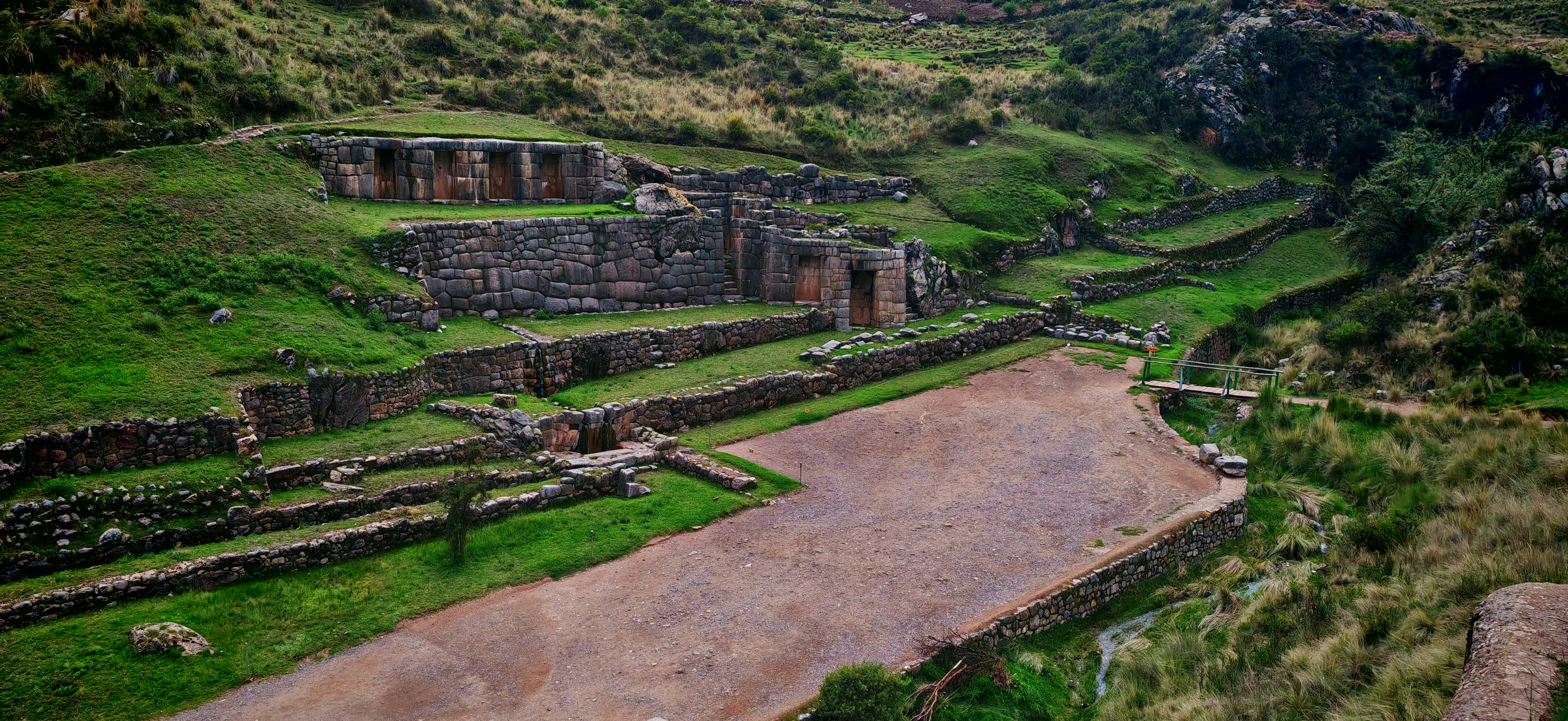 Ancient ruins are nestled in a green, hilly landscape.