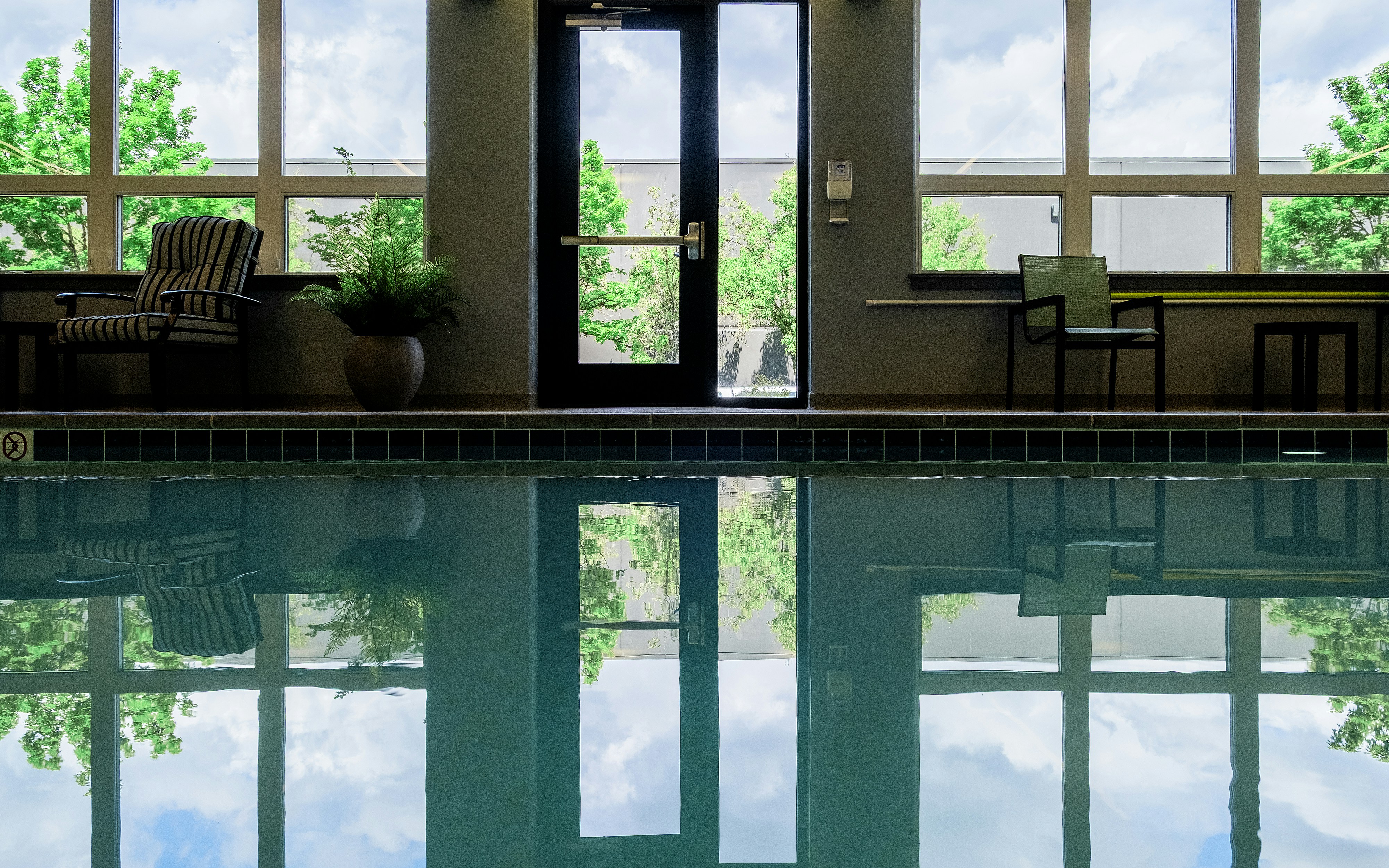 Indoor swimming pool located in apartment complex reflecting a beautiful day outside. | Indoor pool with windows reflecting the outside.