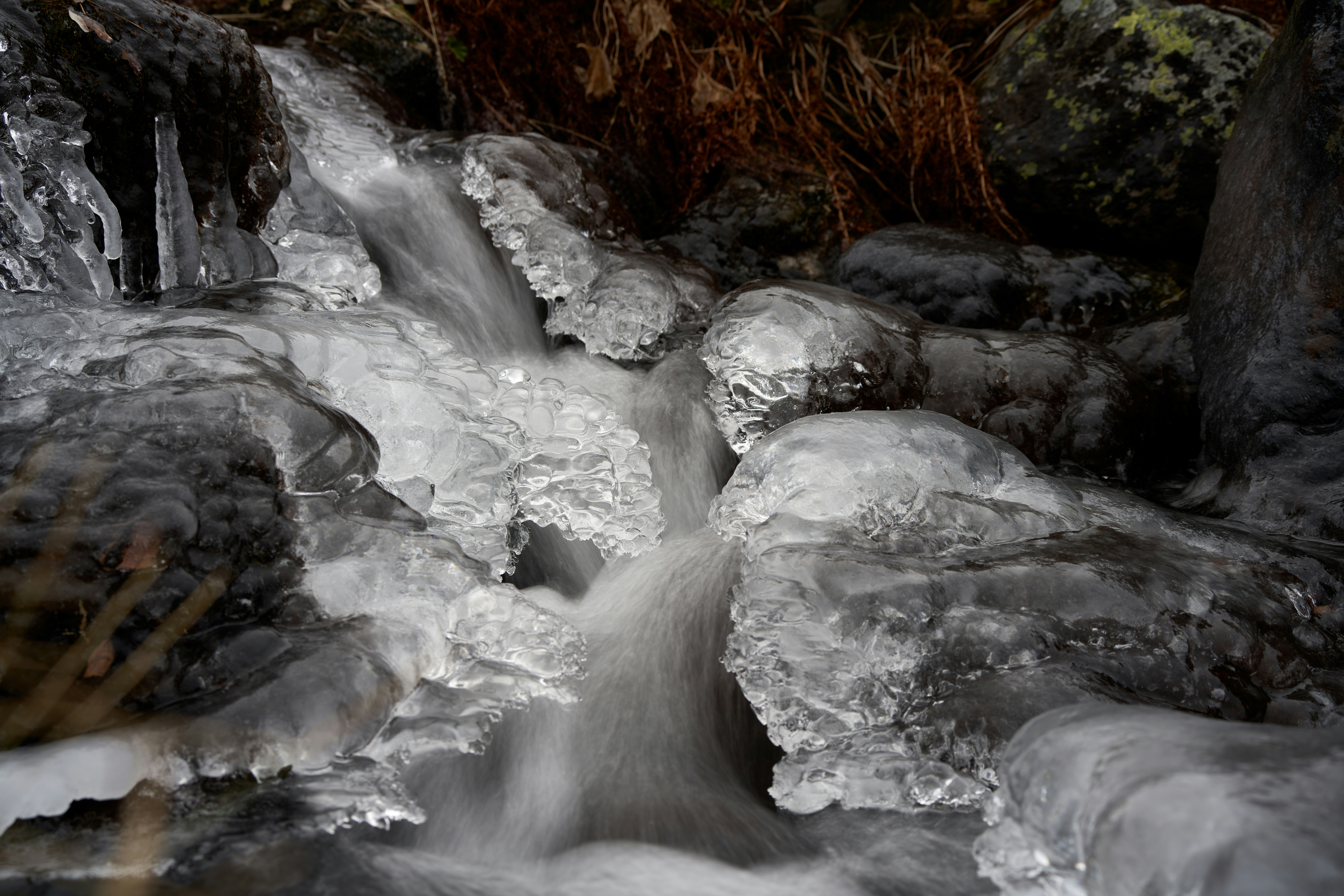Fast mountain spring with ice bobbles. Long exposure. | Water flows over ice-covered rocks.