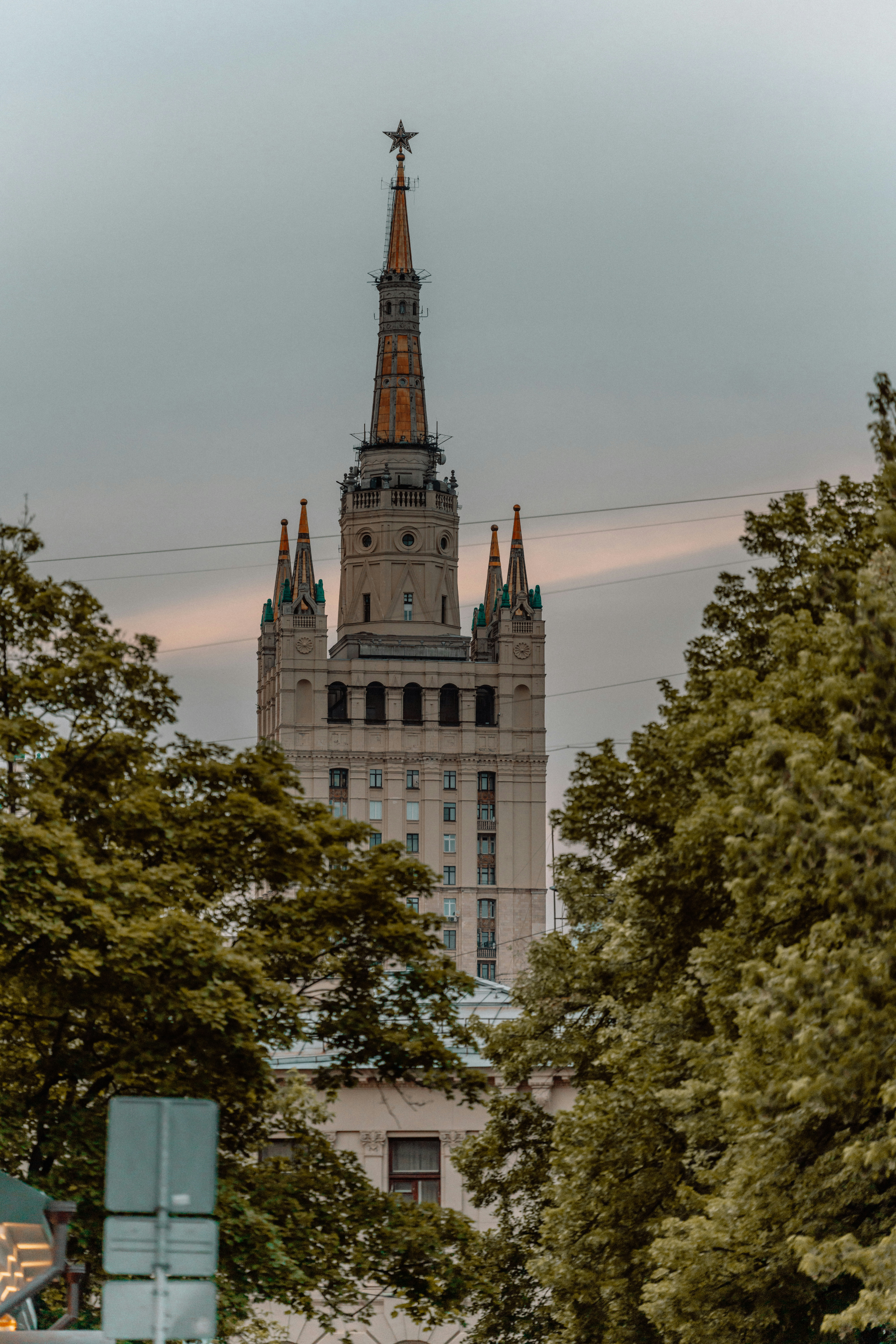 Historic skyscraper featuring a distinctive spire, framed by lush green trees under a moody sky.
