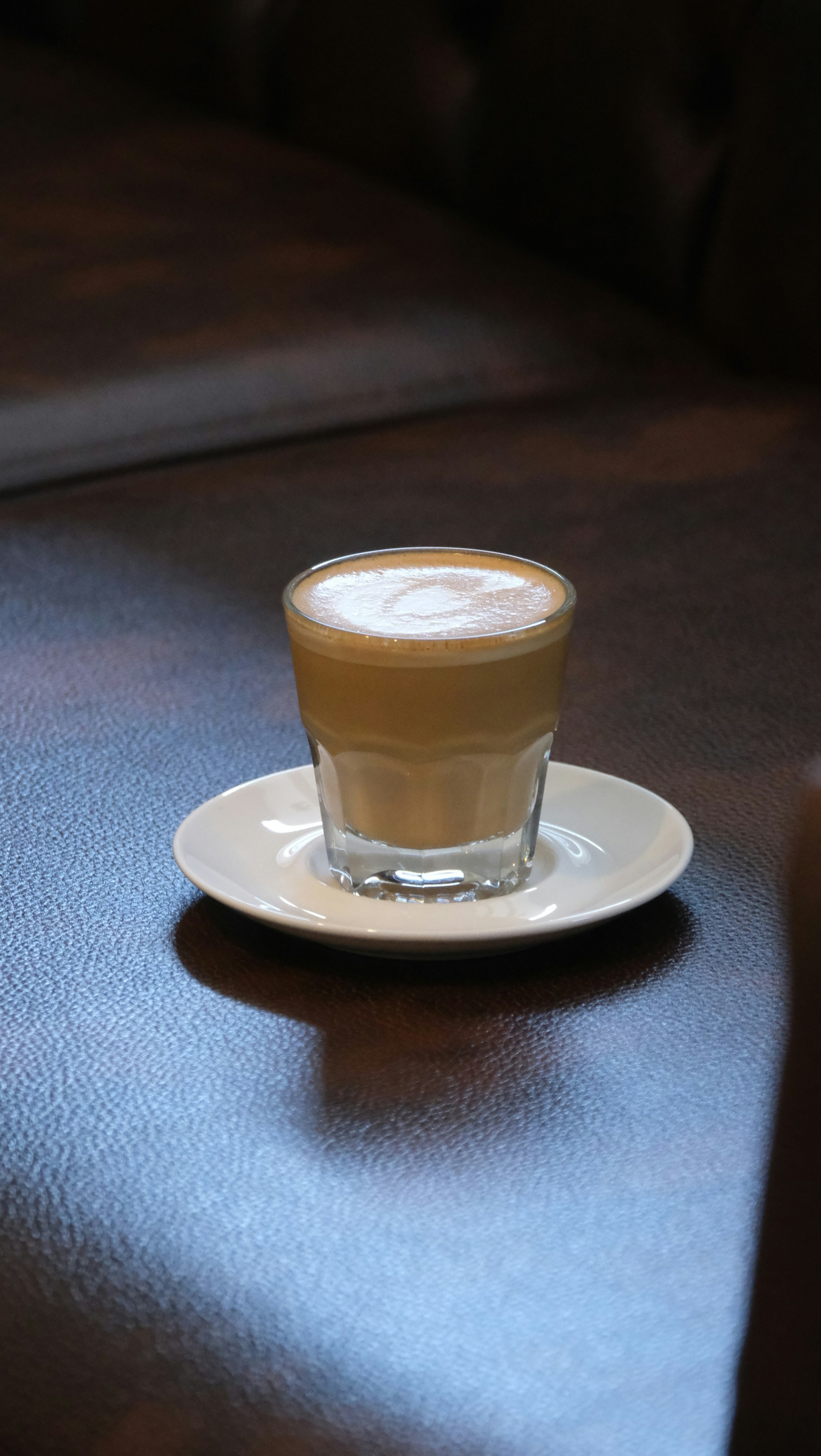 A cortado placed on a moody leather seat corner, bathed in soft daylight.