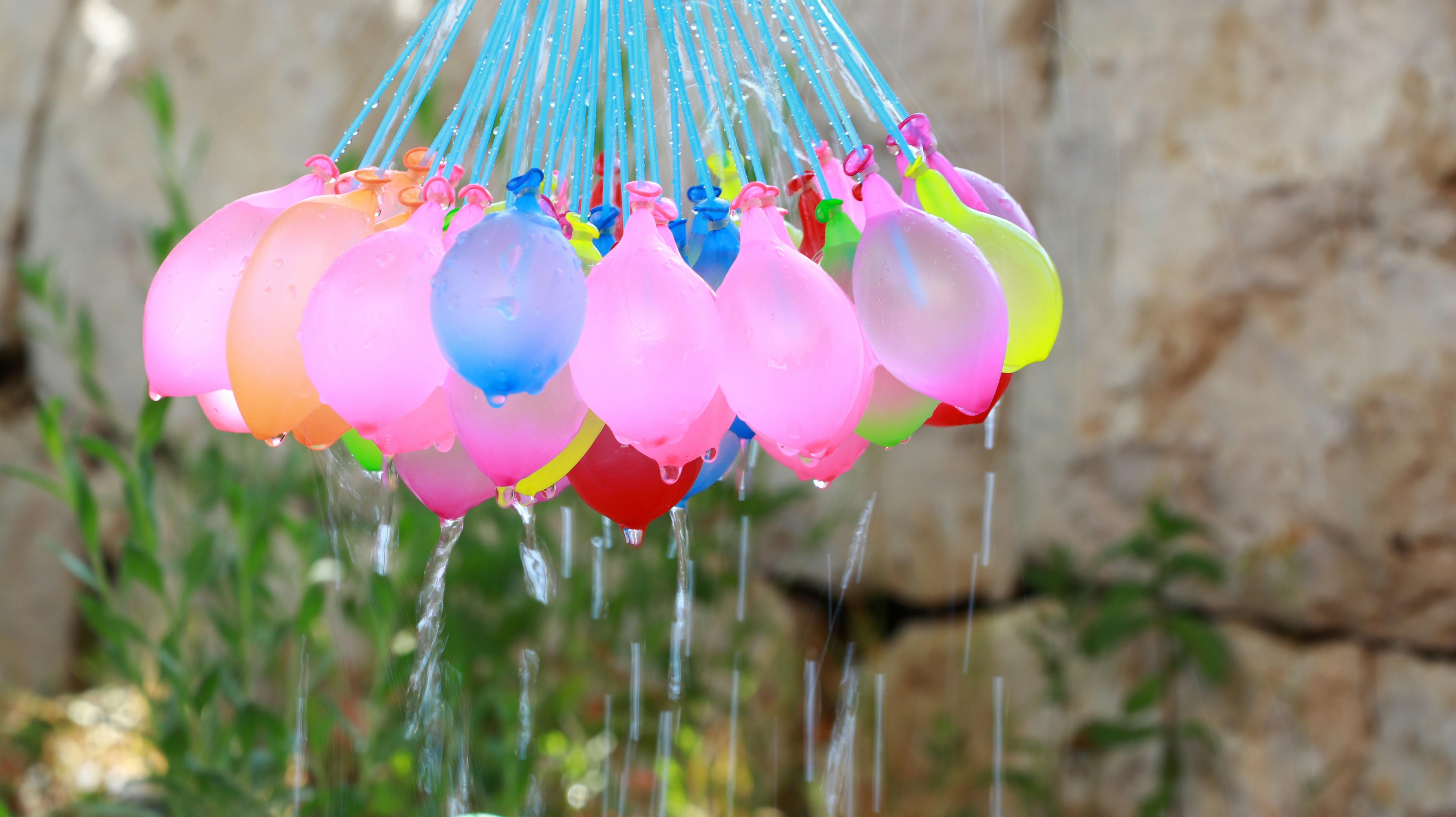 Colorful water balloons suspended and bursting with water, creating a playful scene against a natural backdrop.