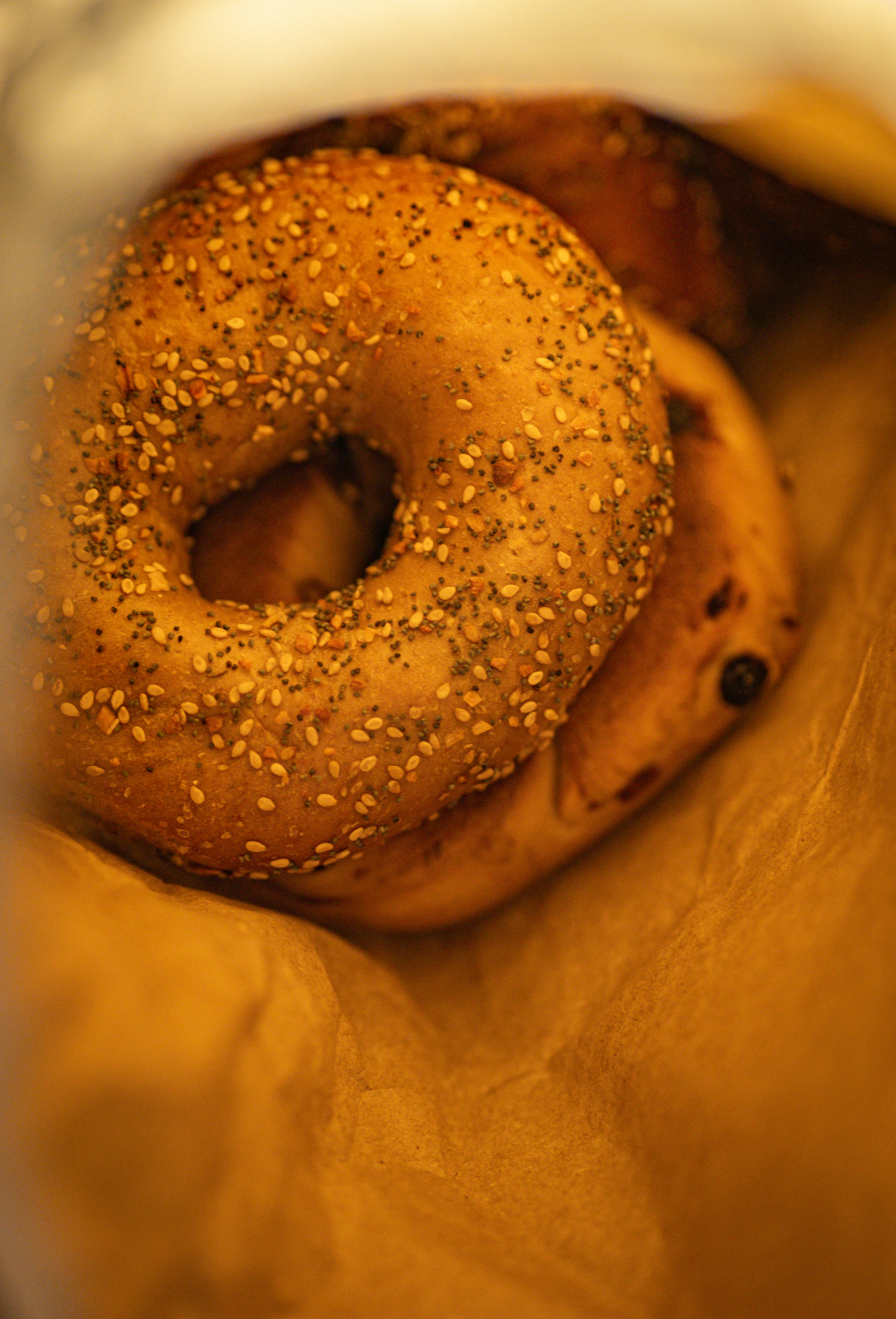 Freshly baked sesame bagel nestled among other baked goods in a paper bag.