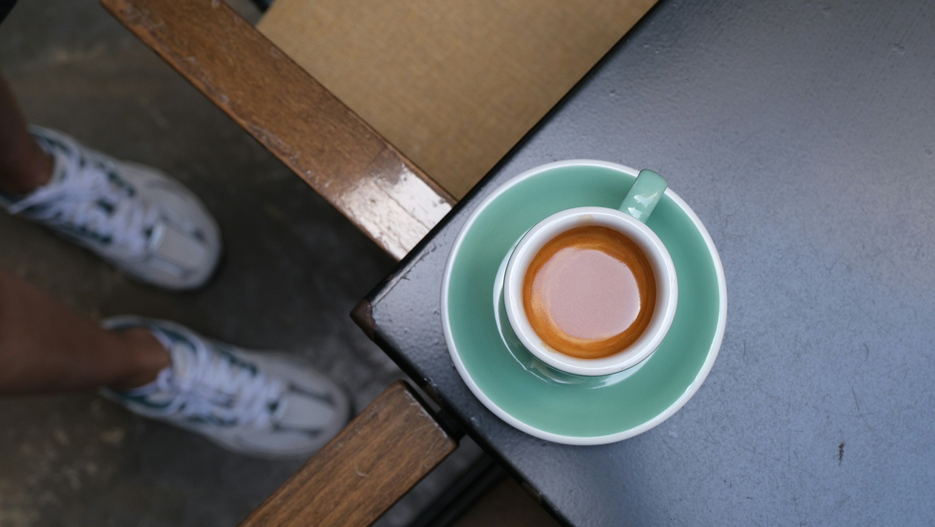 Top-down view of an espresso in a green cup next to a person's foot in casual wear. Raw, spontaneous vibe. | Espresso coffee on a green saucer.