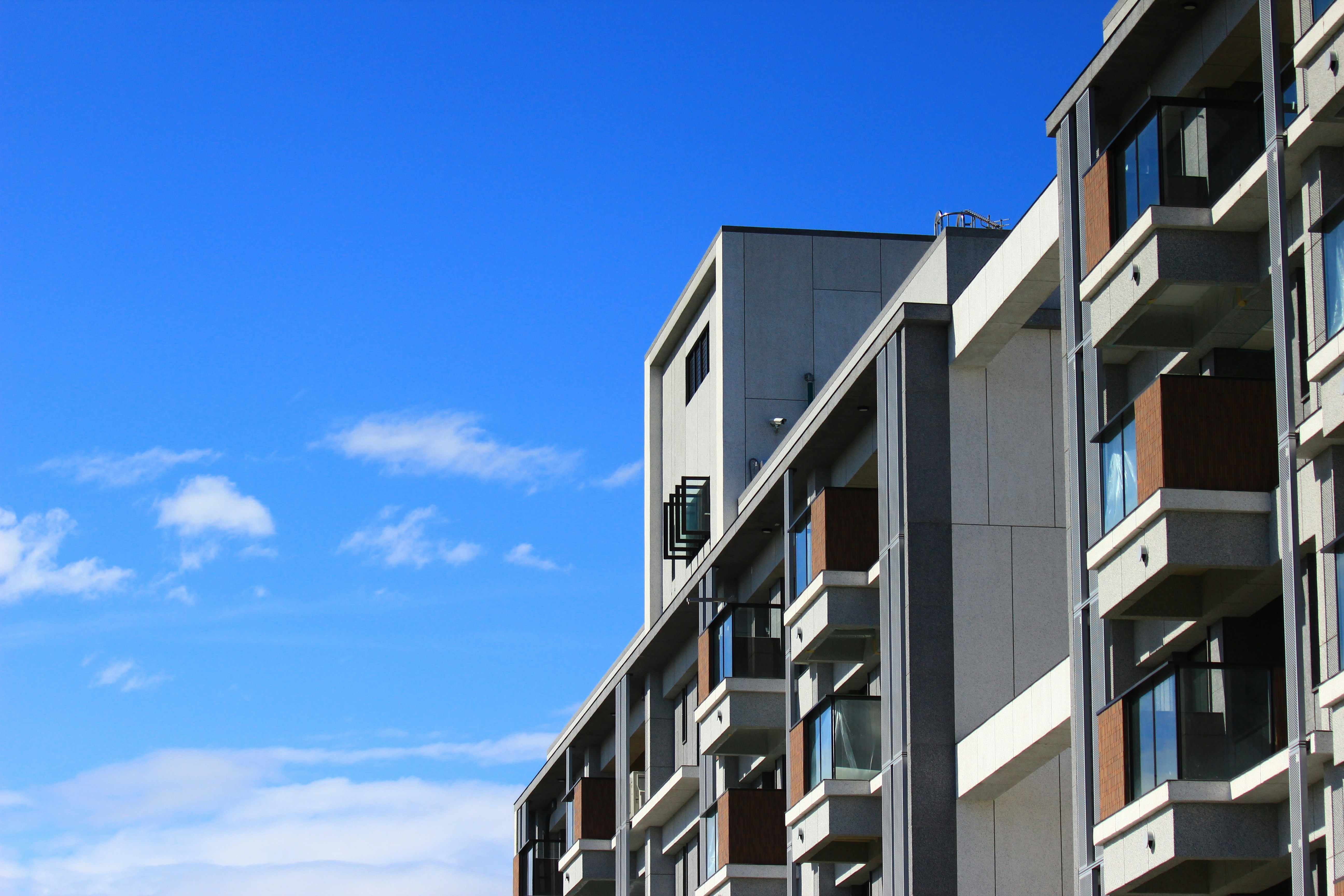 Contemporary apartment building with geometric lines and balconies under a vibrant blue sky.