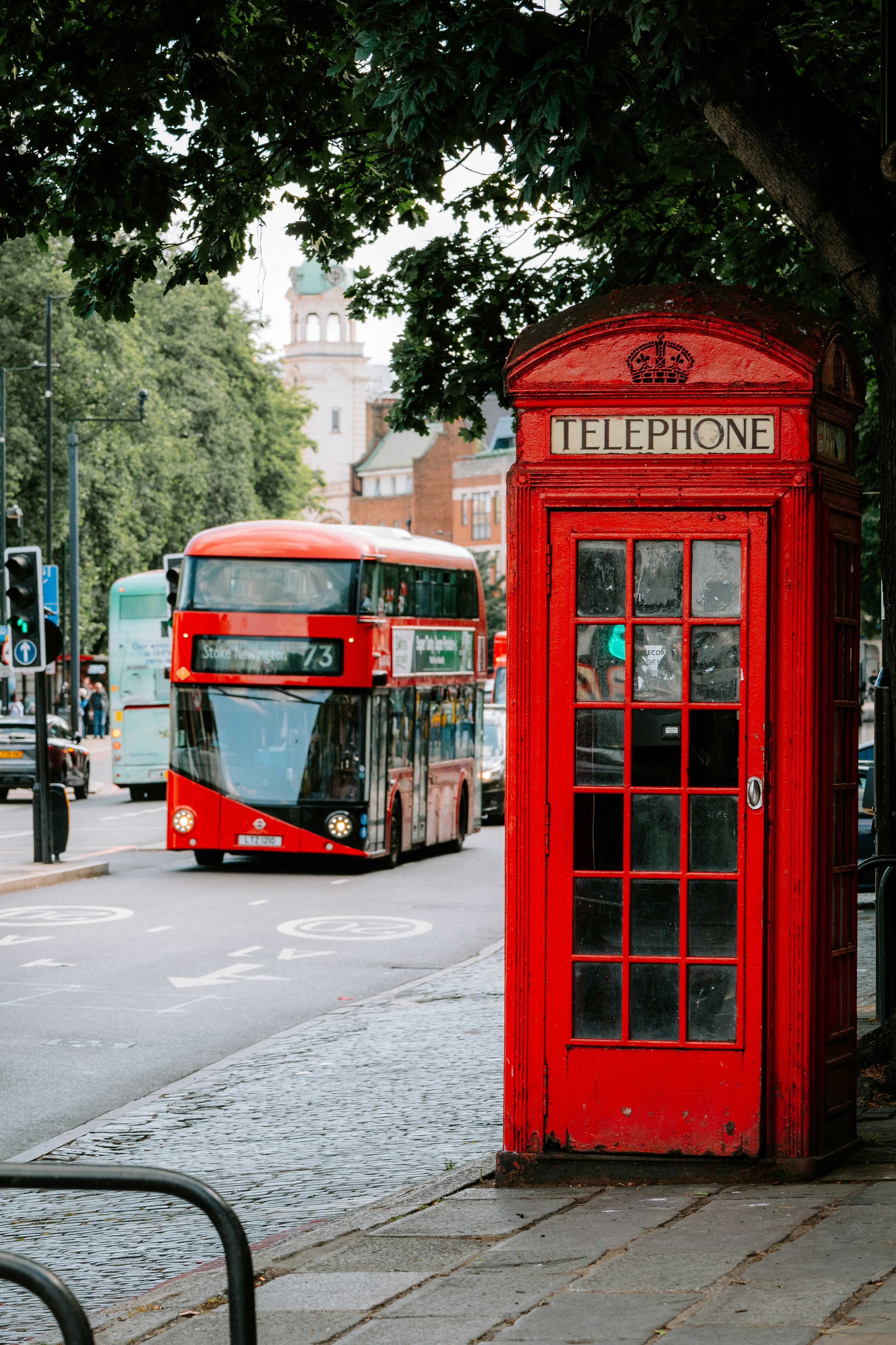 Red telephone booth stands prominently on a city street as a double-decker bus passes by, showcasing urban life and iconic architecture.