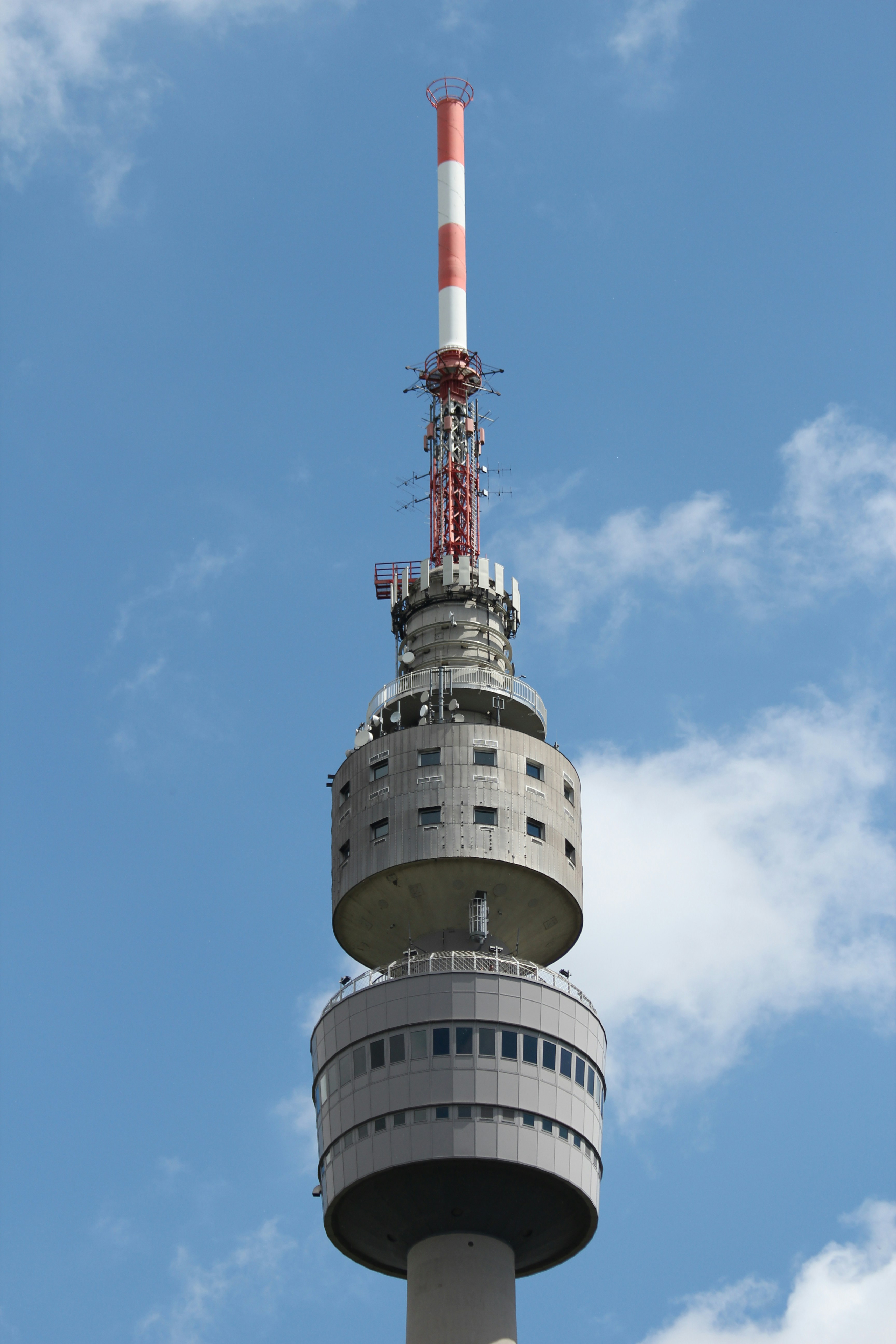 Telecommunications tower reaching into the blue sky, showcasing its intricate design and technology. The structure features a cylindrical base topped with antennas and a vibrant red and white pole.
