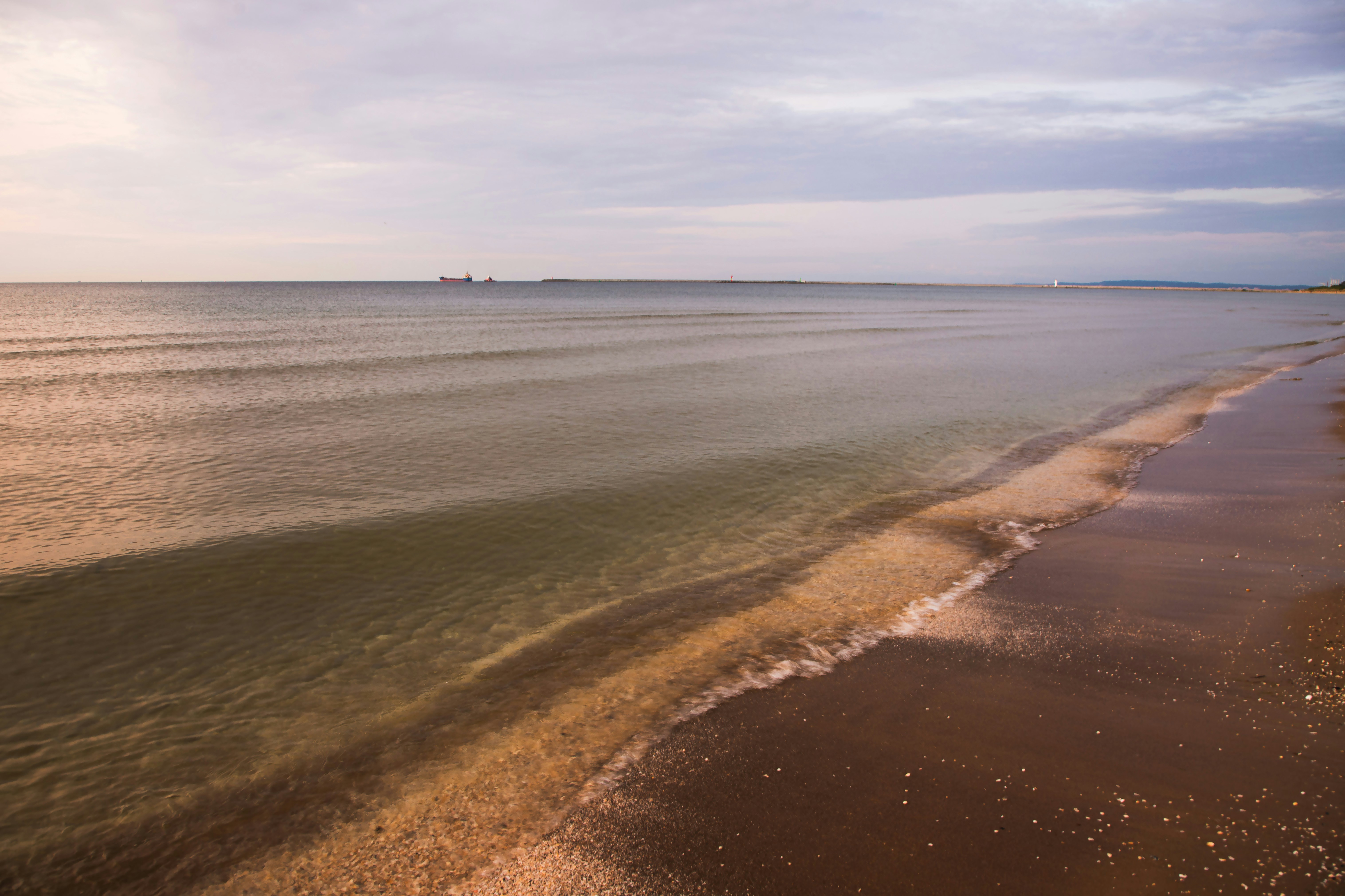 Gentle waves lapping at a sandy shore under a pastel sky, hinting at the calmness of twilight.