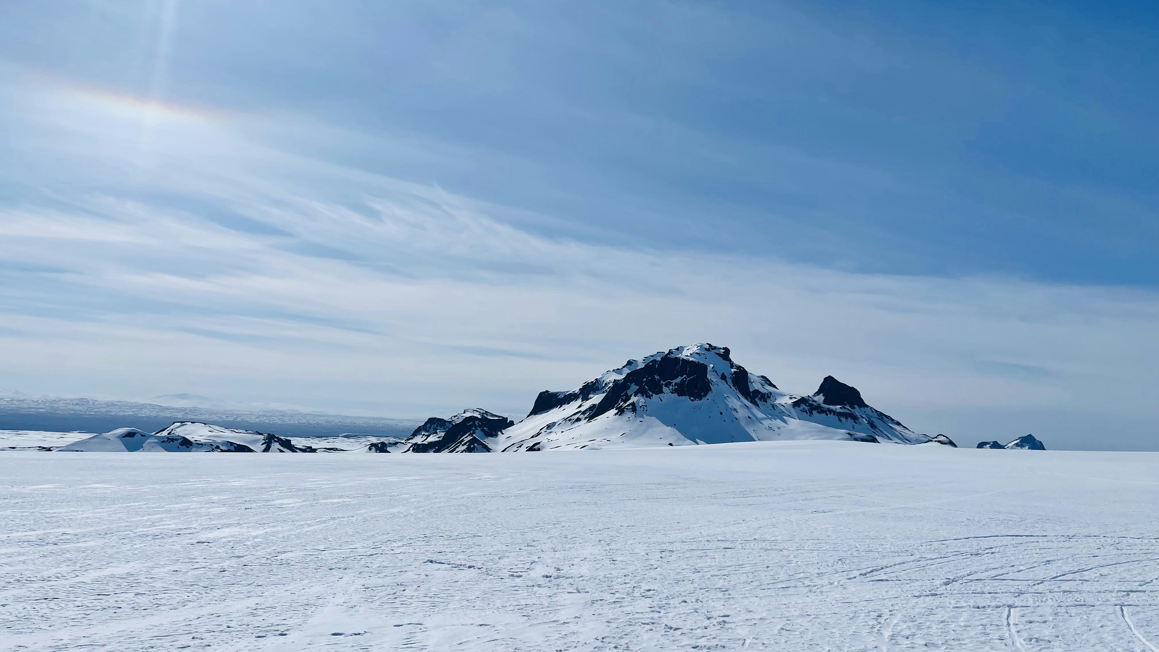 Snow-covered mountain peak rises majestically against a clear blue sky, surrounded by a vast expanse of glistening ice. 