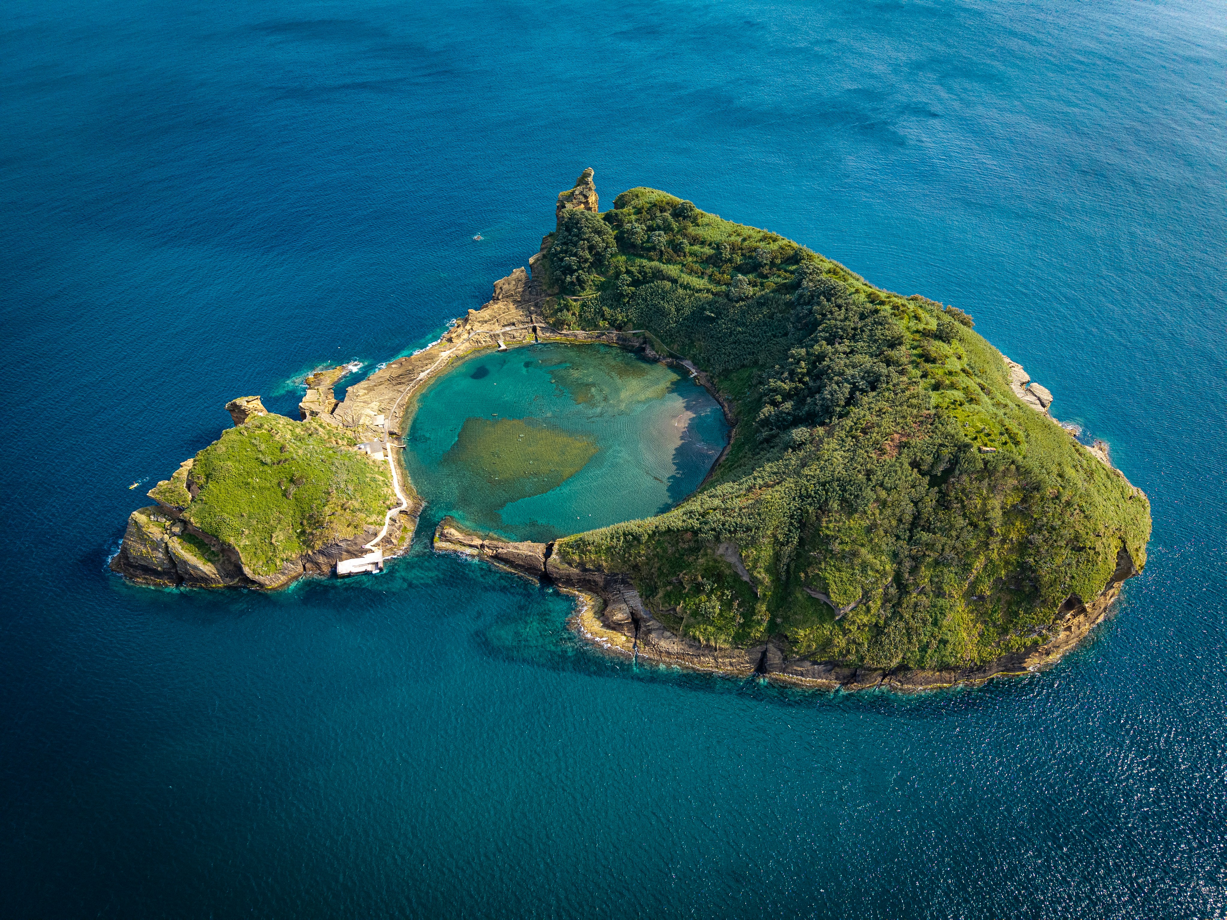Aerial view of a lush, green island featuring a circular lagoon surrounded by rocky shores and vibrant blue waters.