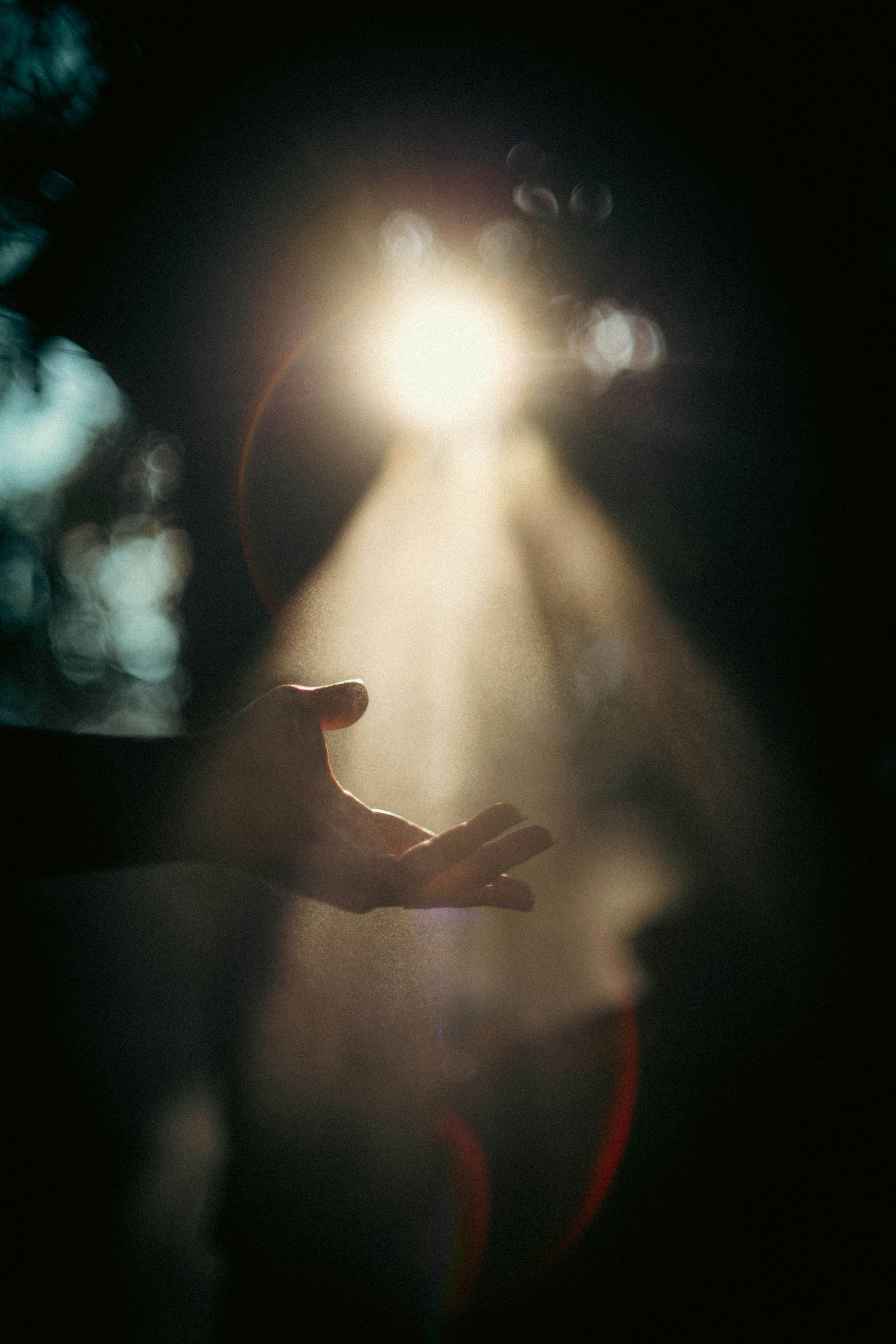 A hand reaches out towards a radiant light source, with particles of dust suspended in the air, creating a magical atmosphere.