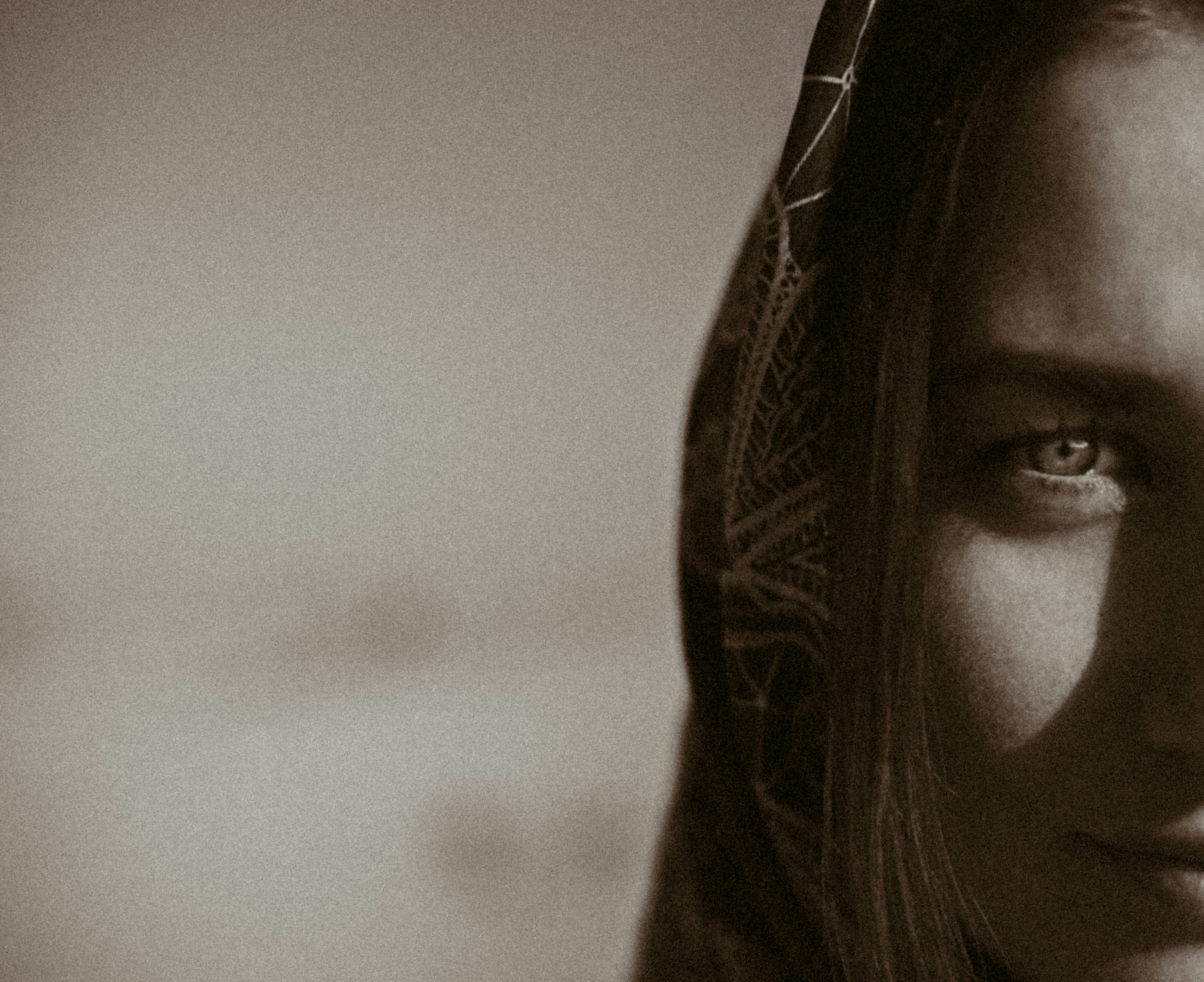 Close-up portrait of a woman with a scarf, her piercing gaze reflecting deep emotion in a sepia-toned setting.