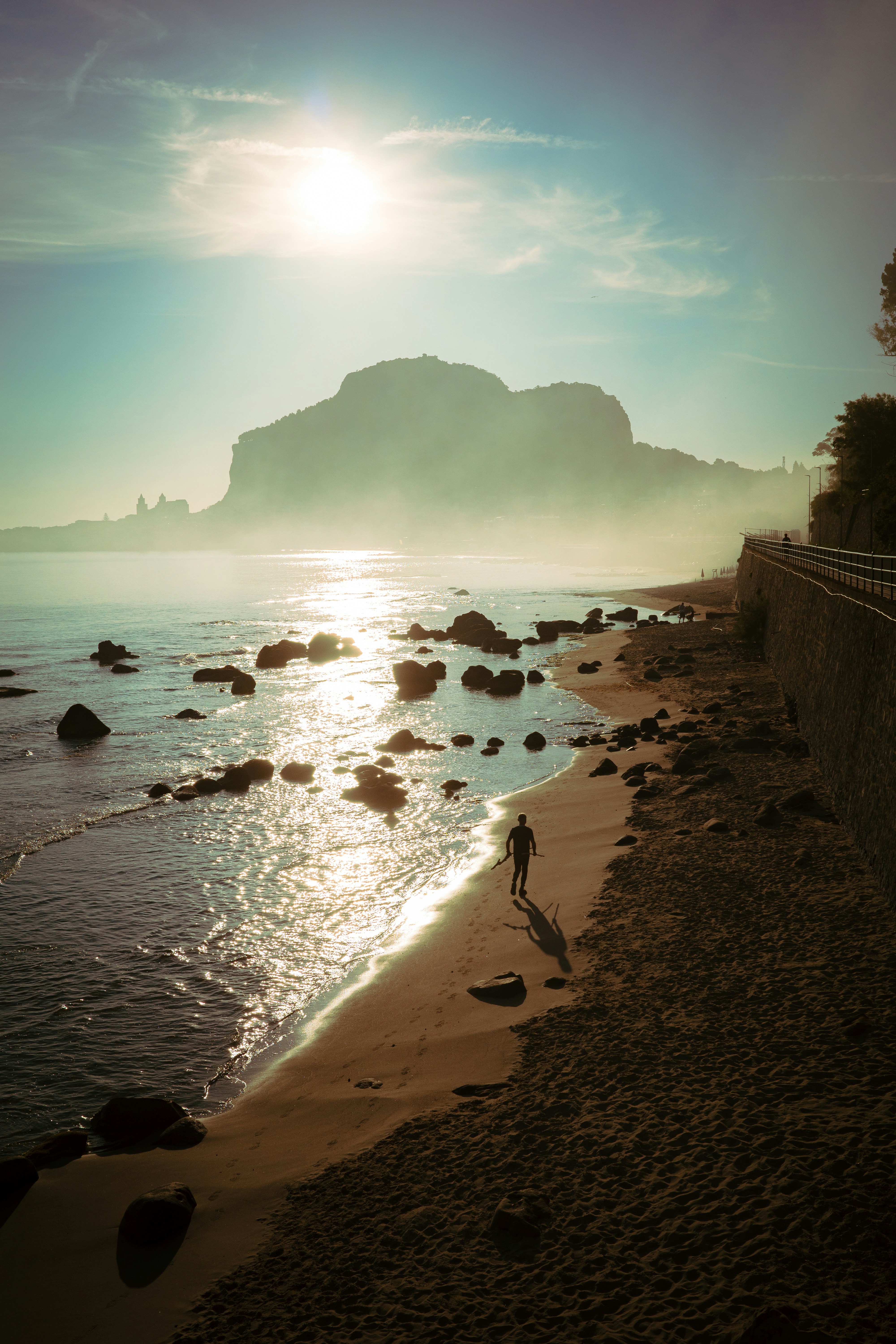 Sunlit Shoreline with Silhouetted Wanderer and Mist-blanketed Formation
