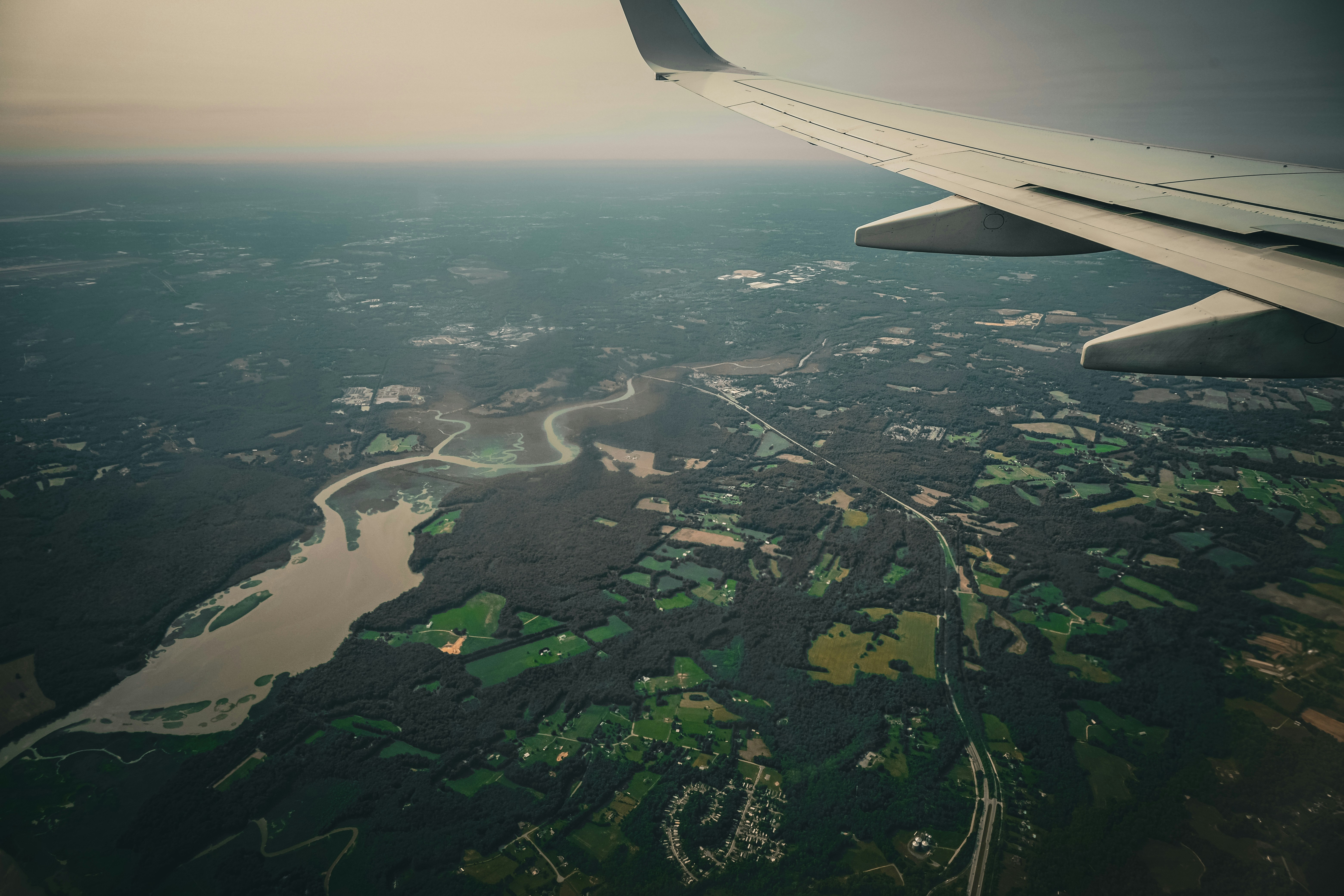 Aerial view showcasing a winding river and lush green fields beneath an airplane wing. The landscape features a blend of water and farmland, illustrating the beauty of nature from above.