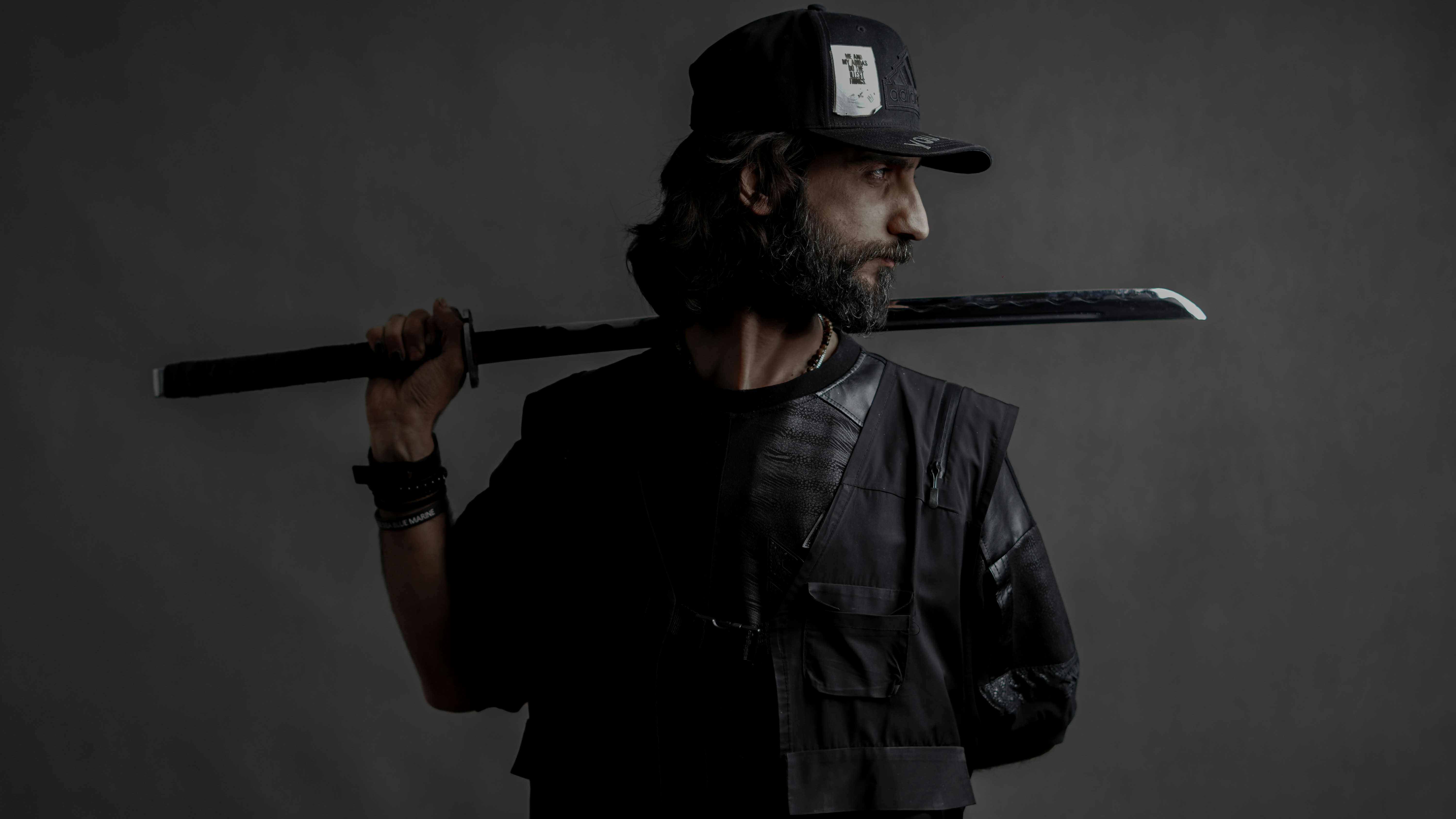 In the shadows, tradition stands tall — a modern silhouette channeling the silent strength of the samurai. Hat low, blade drawn, and discipline etched into every line. NO:03 | A man in black holds a sword.