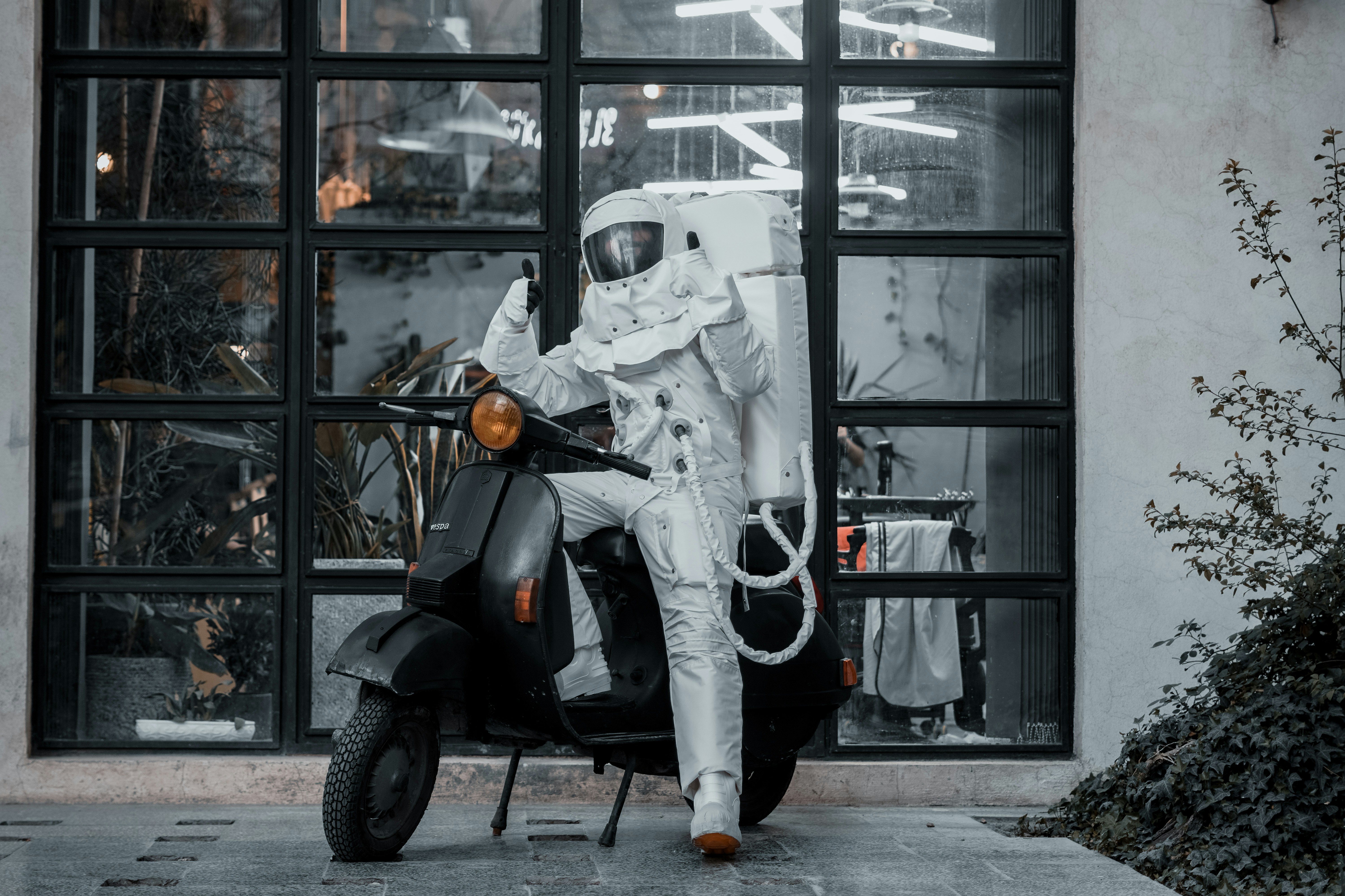 Astronaut and Scooter at a Glass-Front Urban Garage