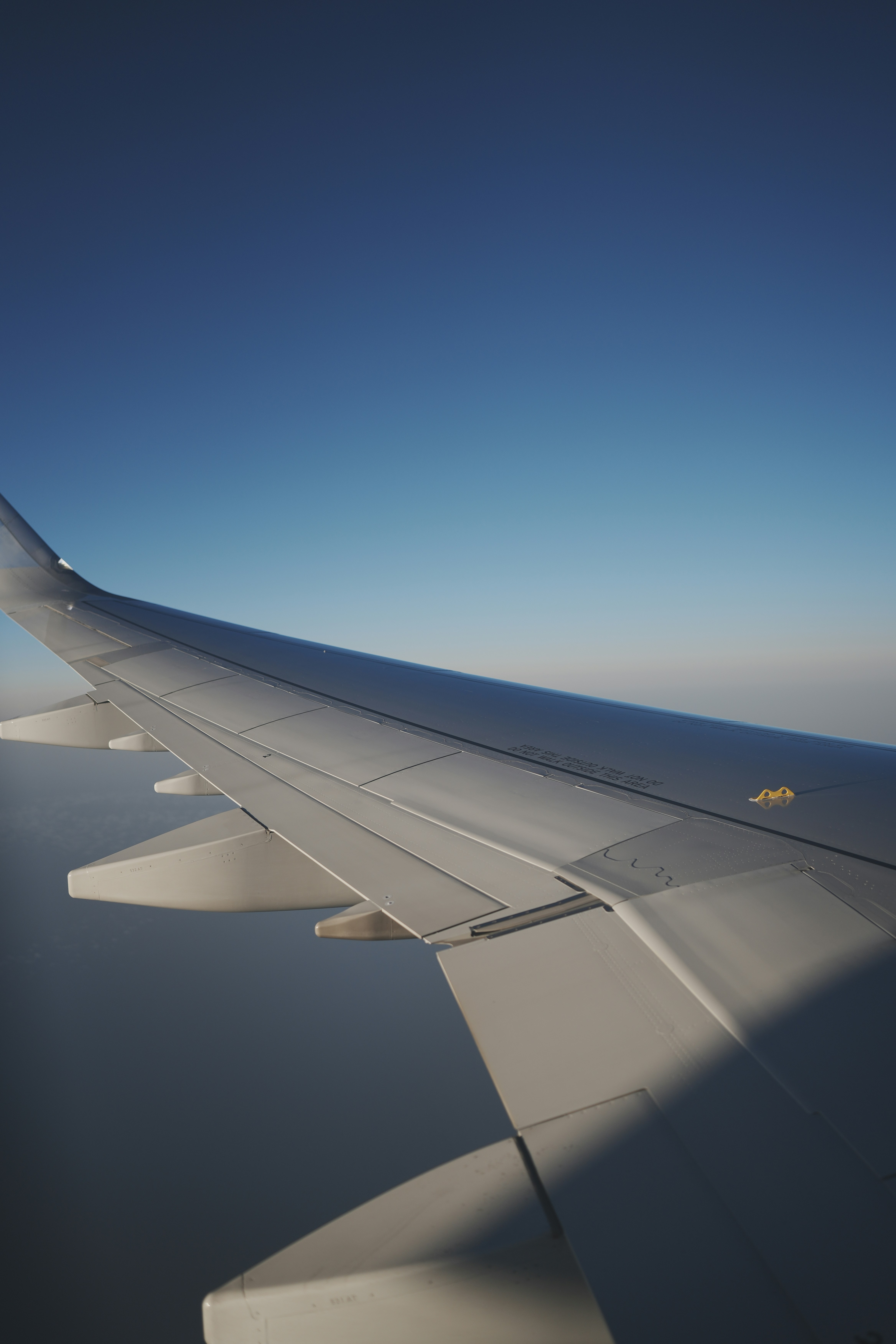 Airplane wing extending into a clear blue sky with soft gradients of light. The scene captures the tranquility of flight.
