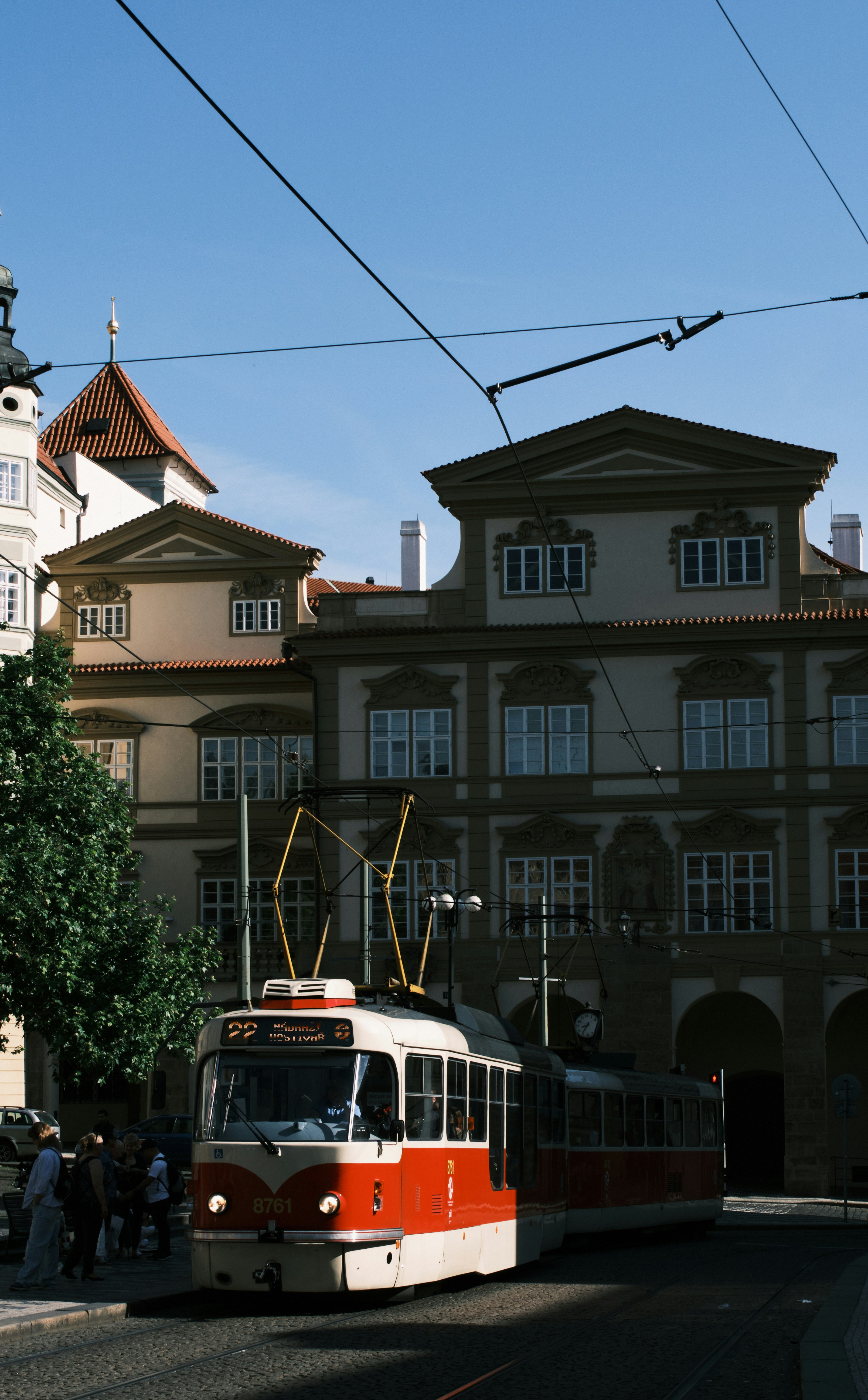 Vintage red tram navigating through a historic city square, framed by classical architecture and vibrant greenery.