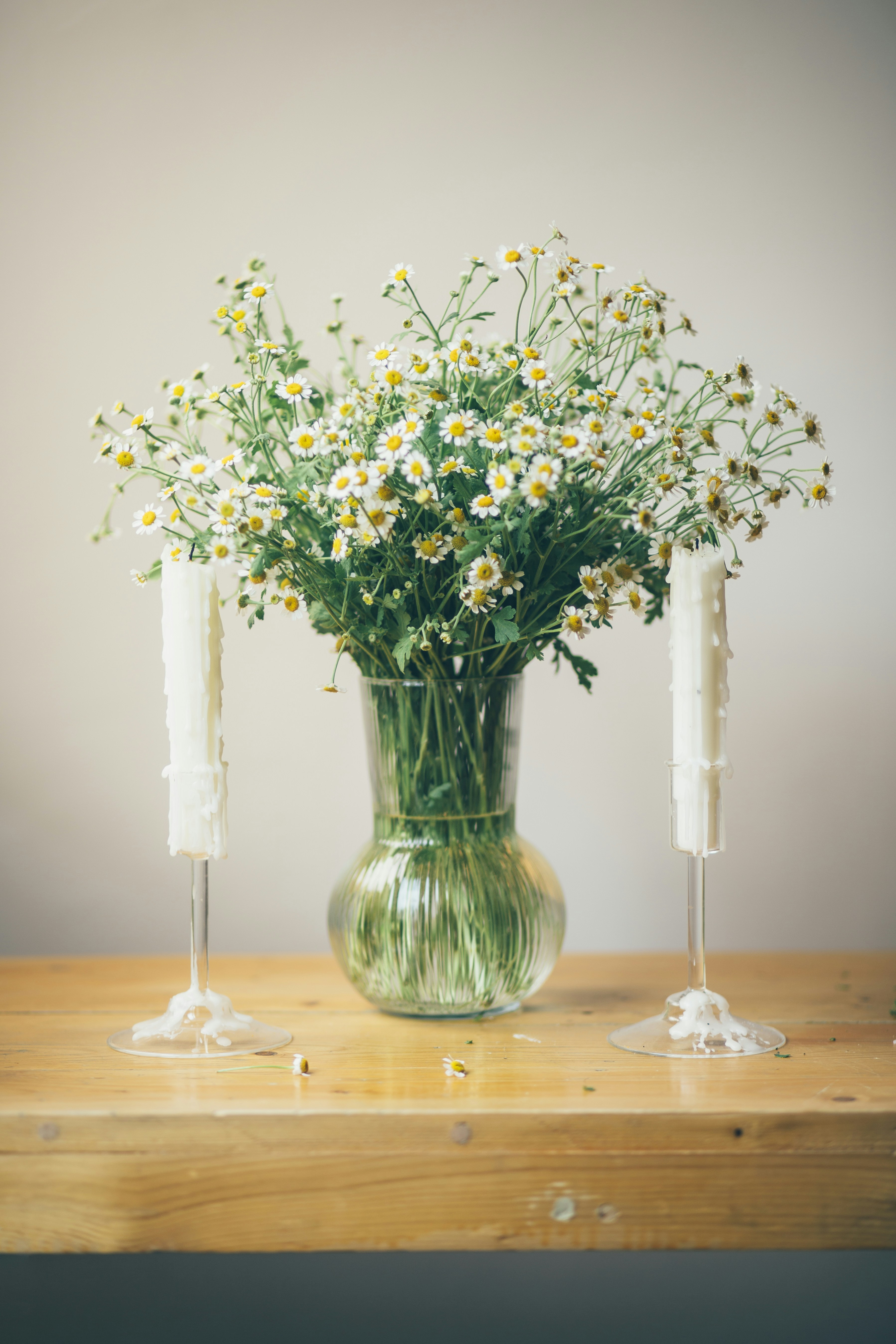 Vibrant bouquet of daisies in a glass vase flanked by elegant white candles on a wooden table. 