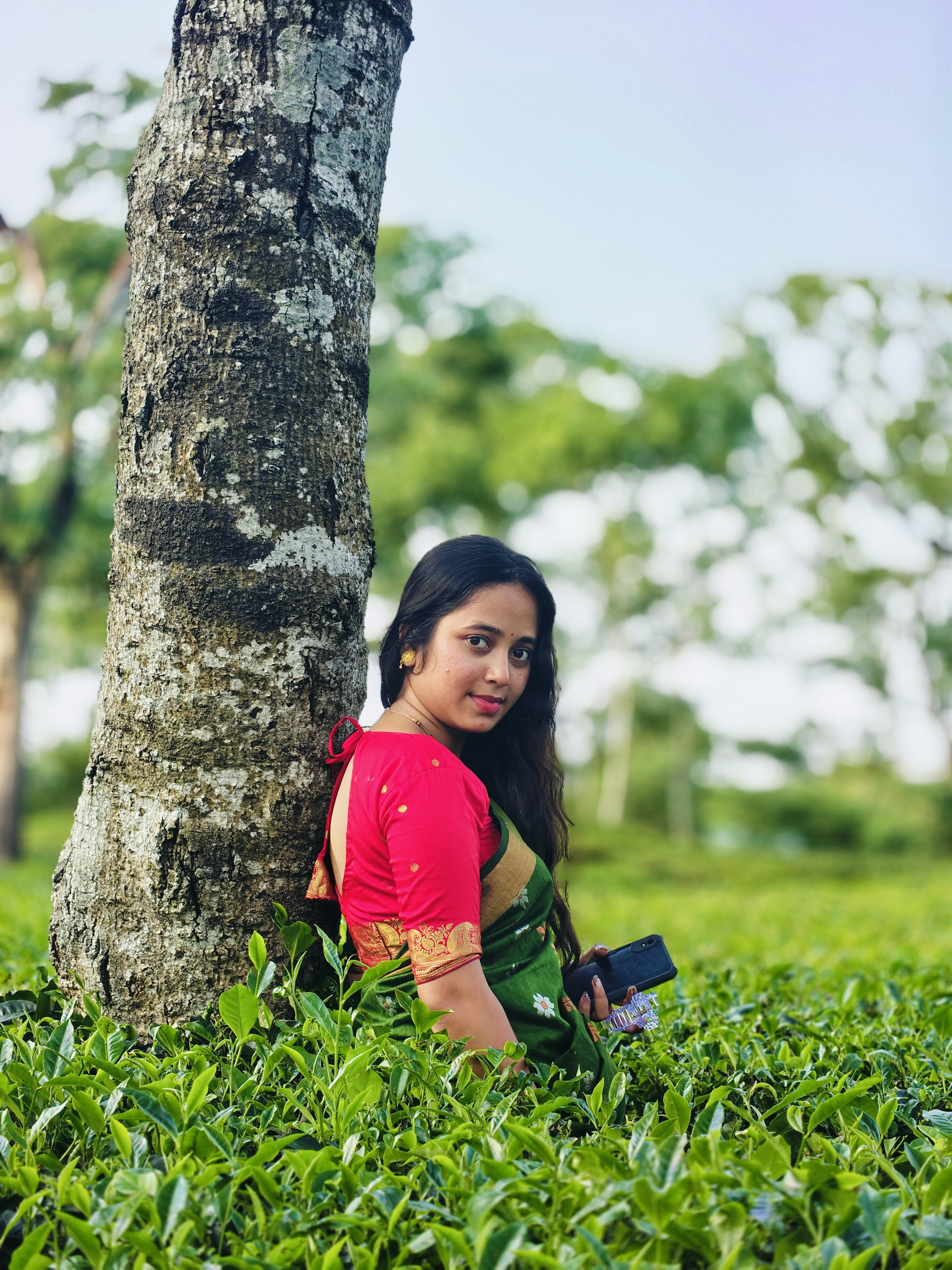 Portrait by the Mossy Trunk: A Red-Blouse Moment in a Sunlit Green Field