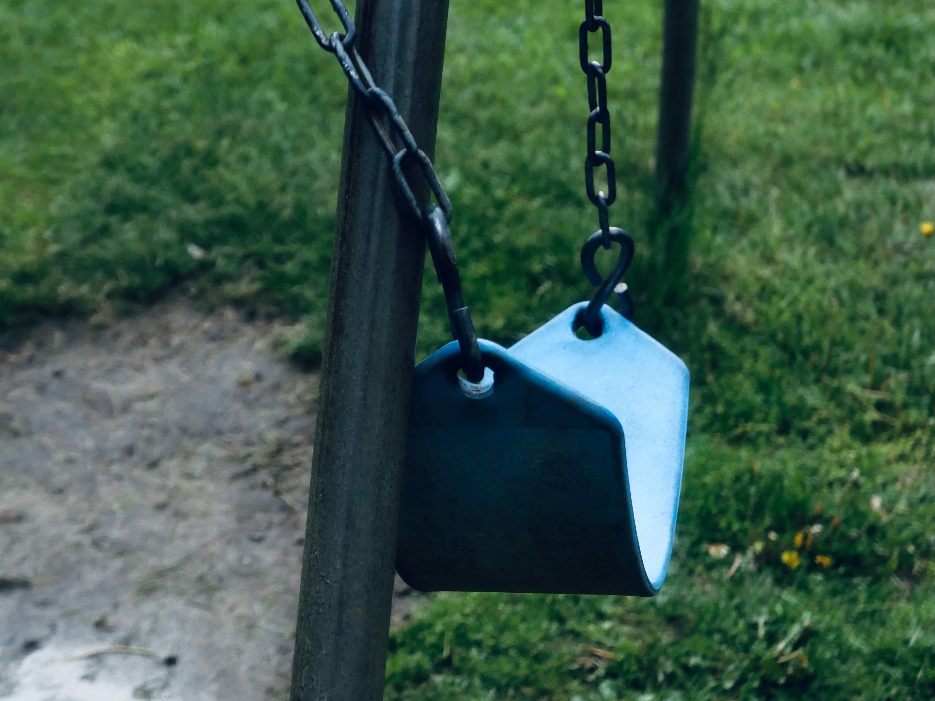A blue swing hanging from a chain, captured in a tranquil playground setting surrounded by lush grass.