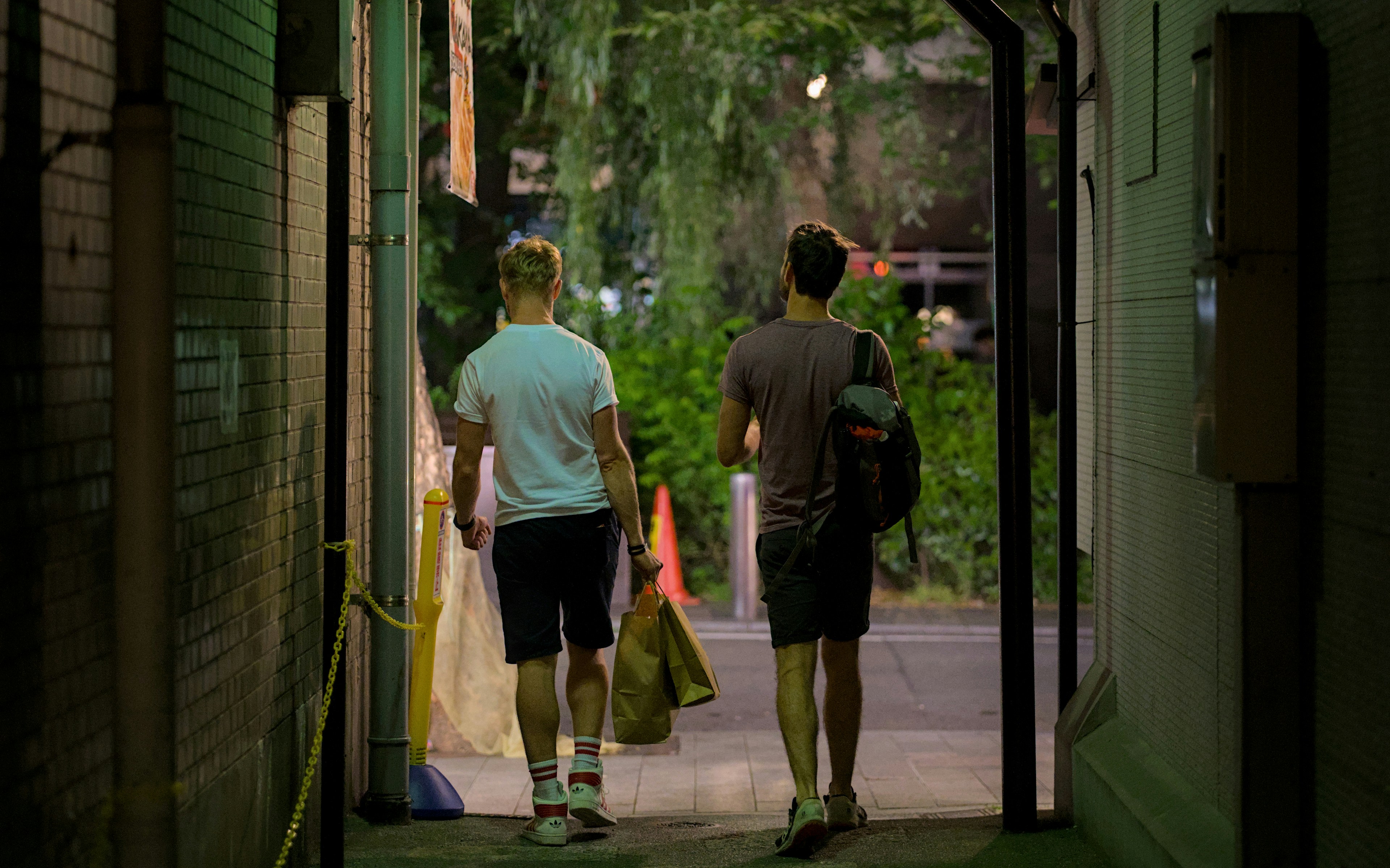 Two Shoppers Leave a Narrow Green-Walled Alley into Daylight
