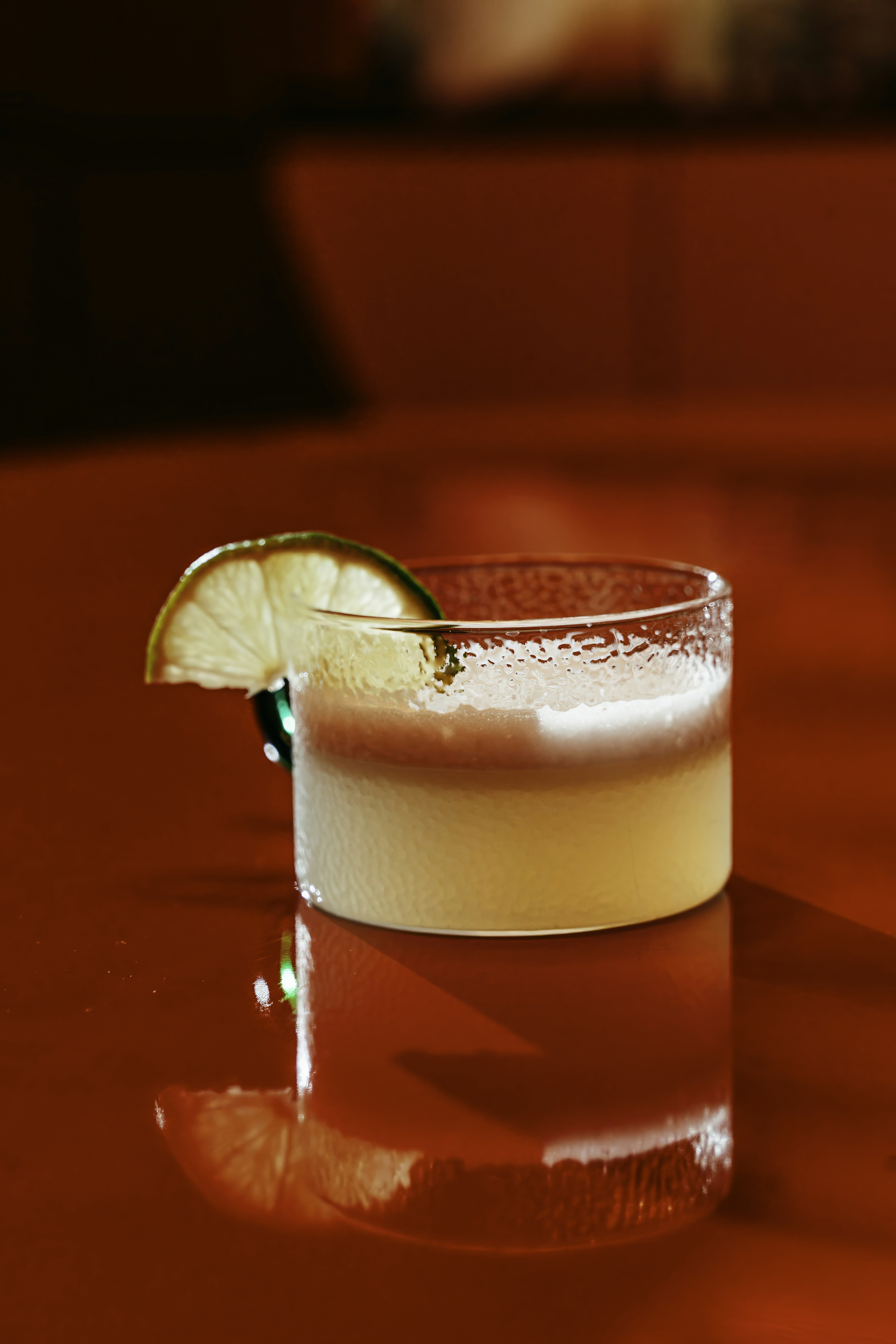 Crimson Glow: Lime-Wedged Cocktail on a Reflective Red Bar