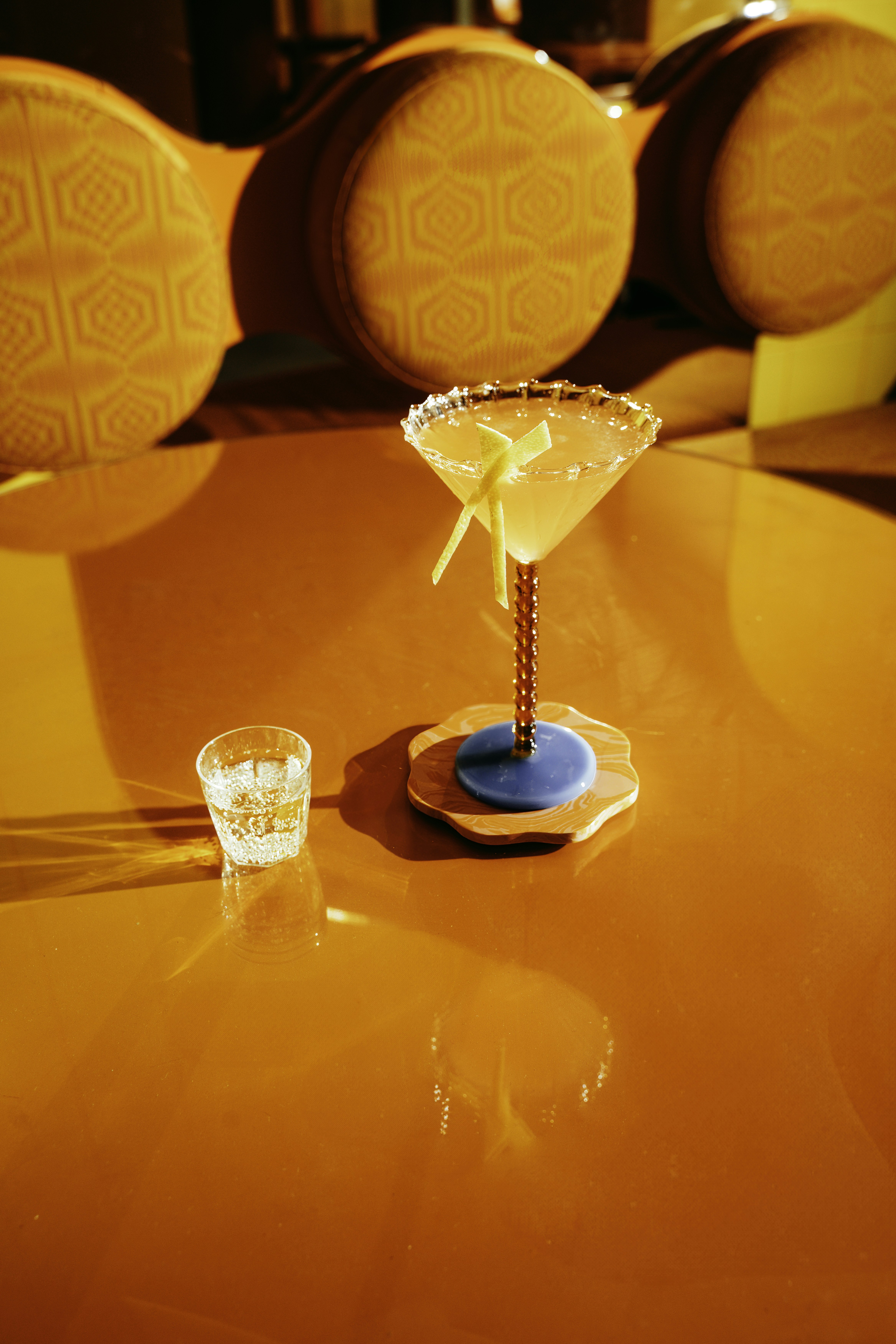 A martini and a shot on a vibrant orange surface.