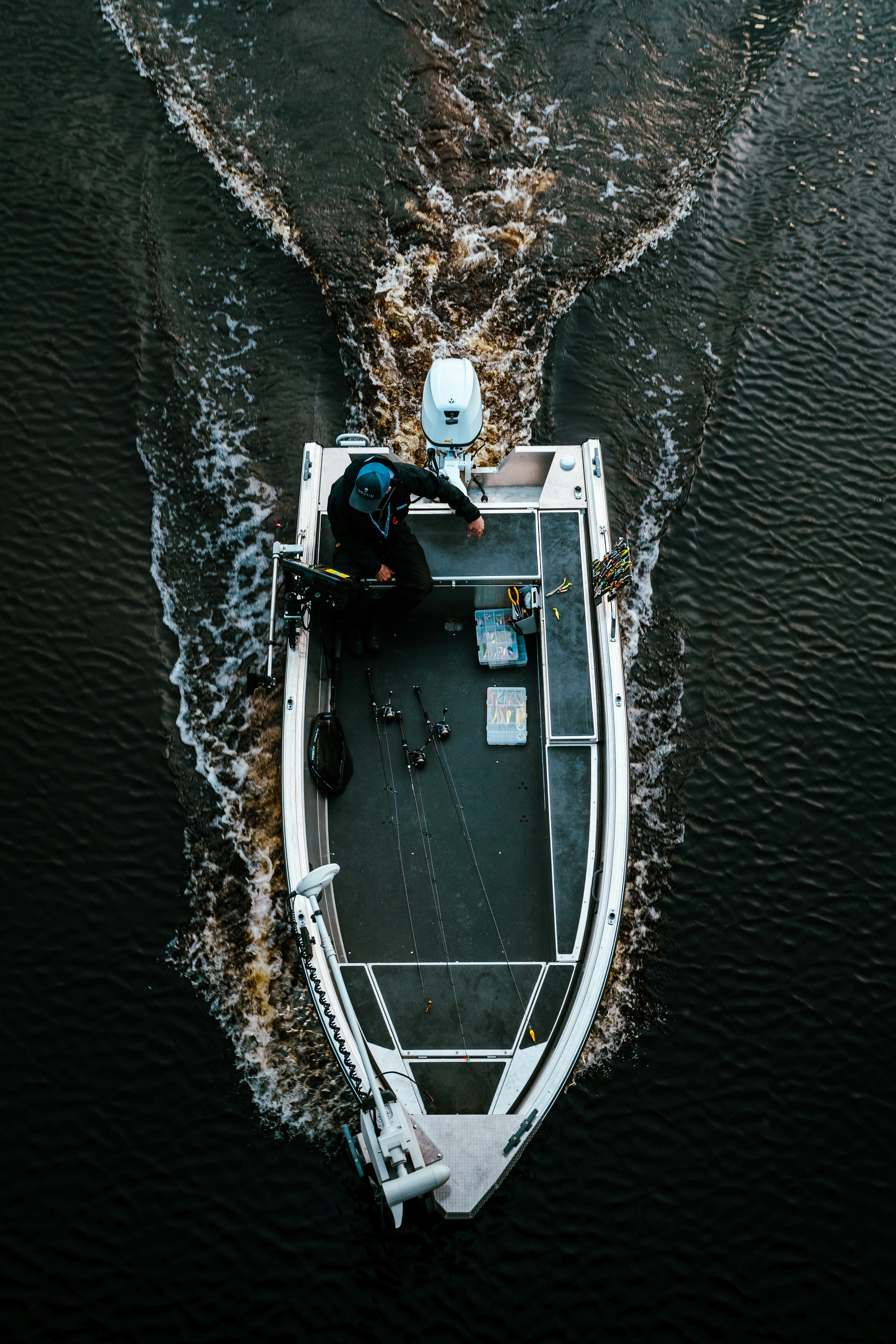 A fisherman skillfully maneuvers a small boat through calm waters, surrounded by ripples and reflections. Fishing rods and tackle are neatly arranged on the boat's deck.