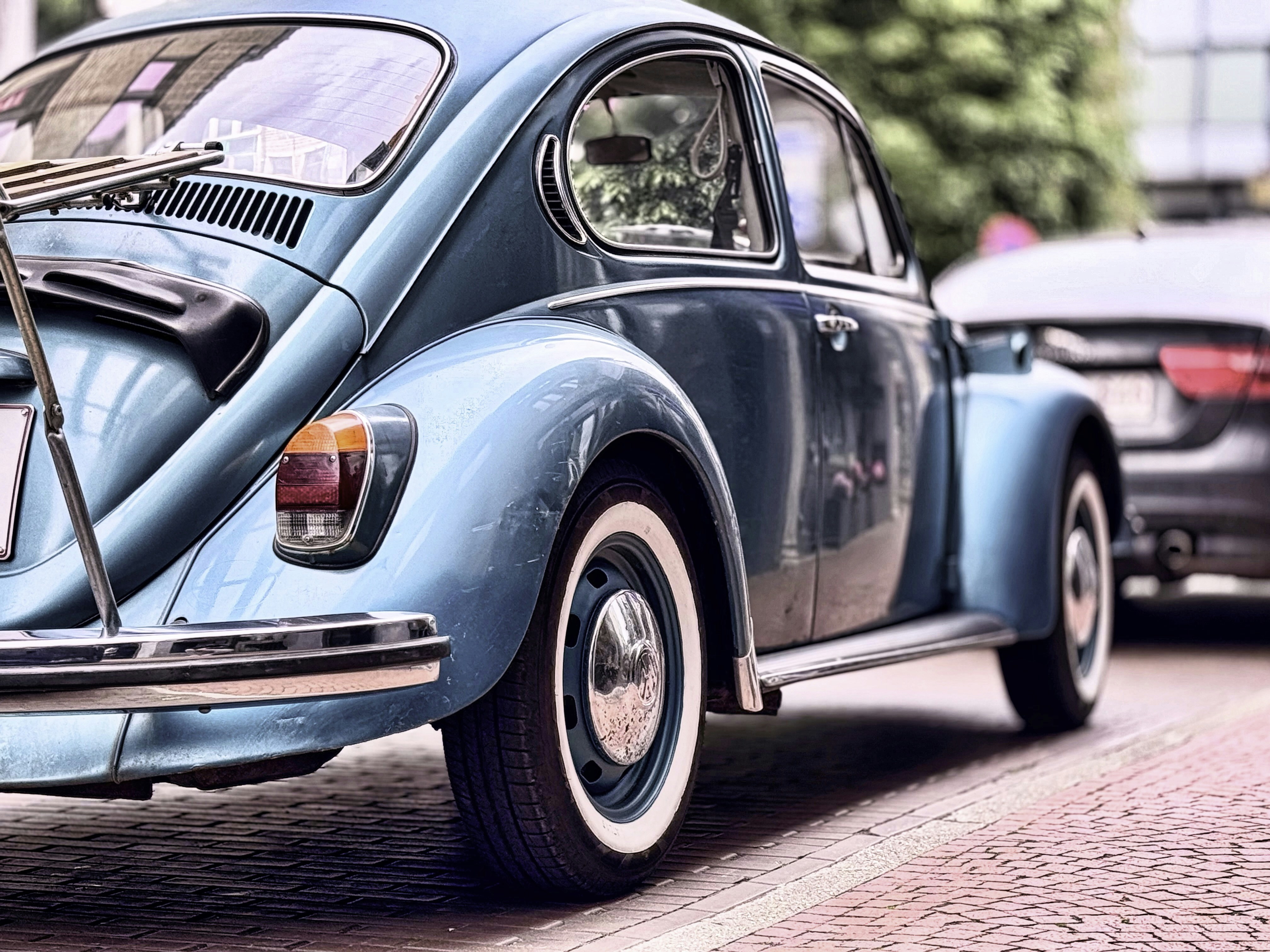 Vintage blue Volkswagen Beetle parked beside a modern car, showcasing a blend of classic and contemporary automotive design.