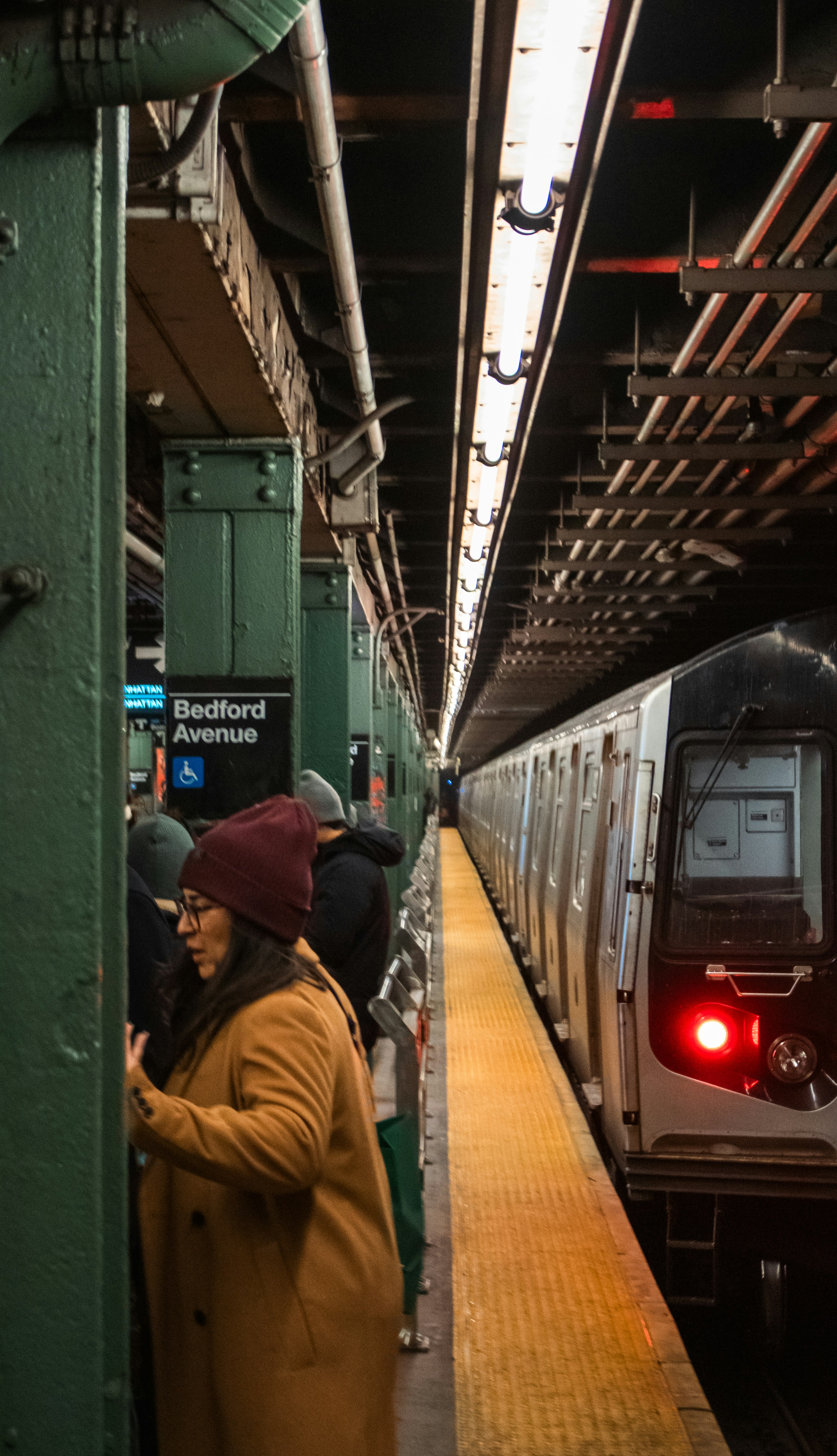 An NYC MTA subway train sits at the platform with its doors closed, moments before departure. Commuters who exited the train are seen walking along the platform toward station exits. The image captures a common moment in the city’s transit rhythm—between arrival and departure—highlighting the movement of people and the function of public transportation in daily urban life.