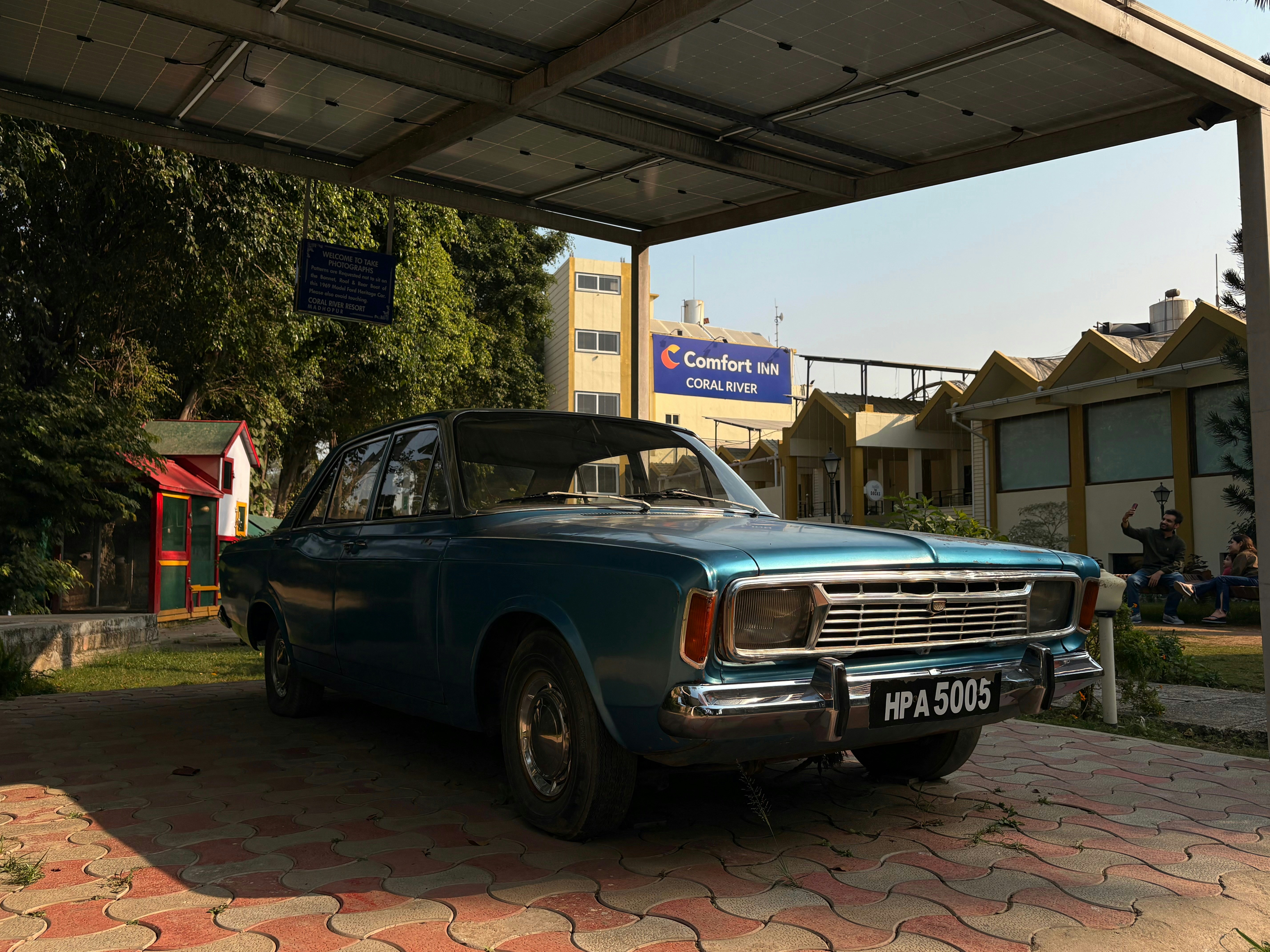 Sunlit nostalgia: blue vintage sedan under a roadside canopy