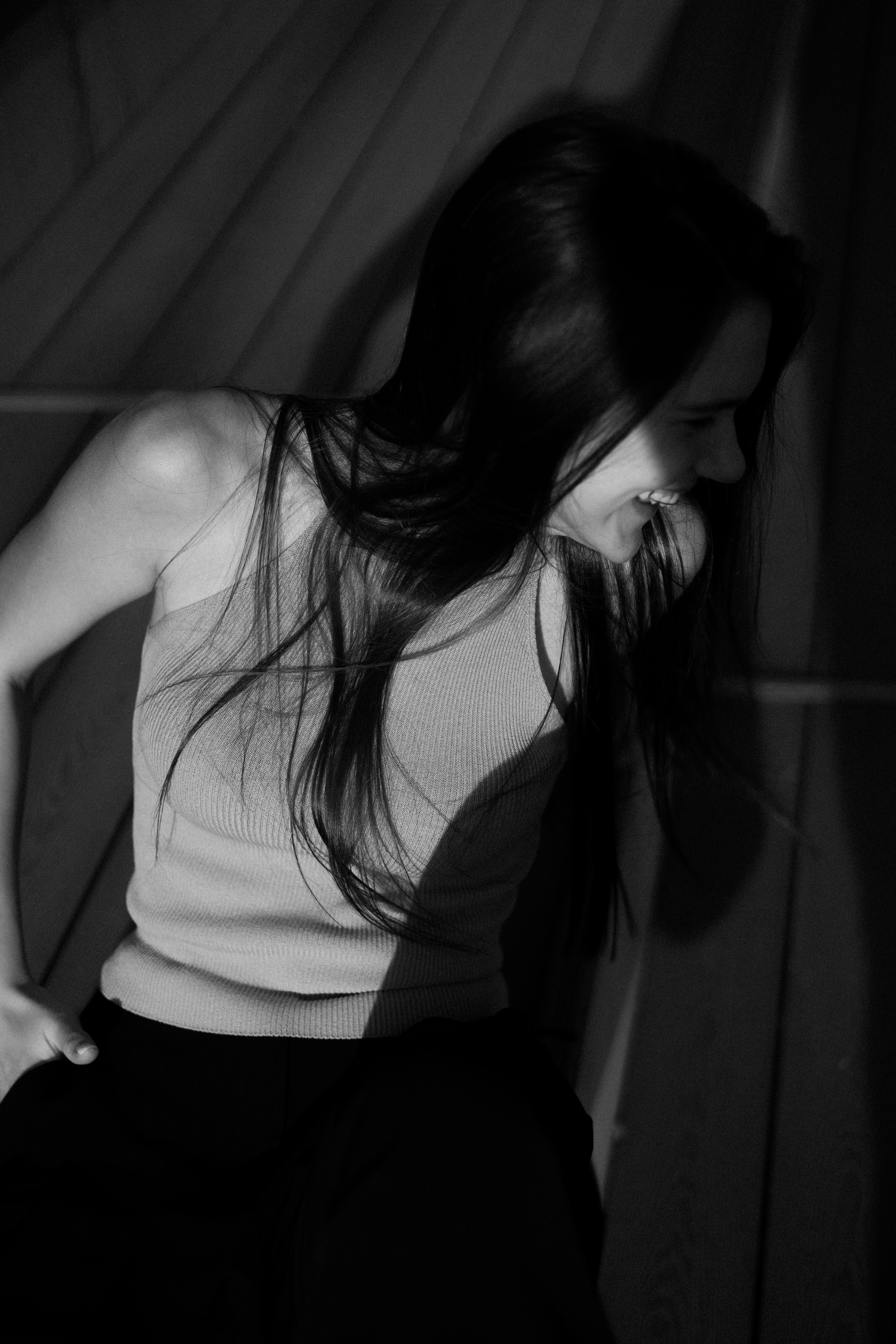 A woman with long hair smiles softly, partially illuminated against a backdrop of diagonal lines, creating a dynamic interplay of light and shadow.