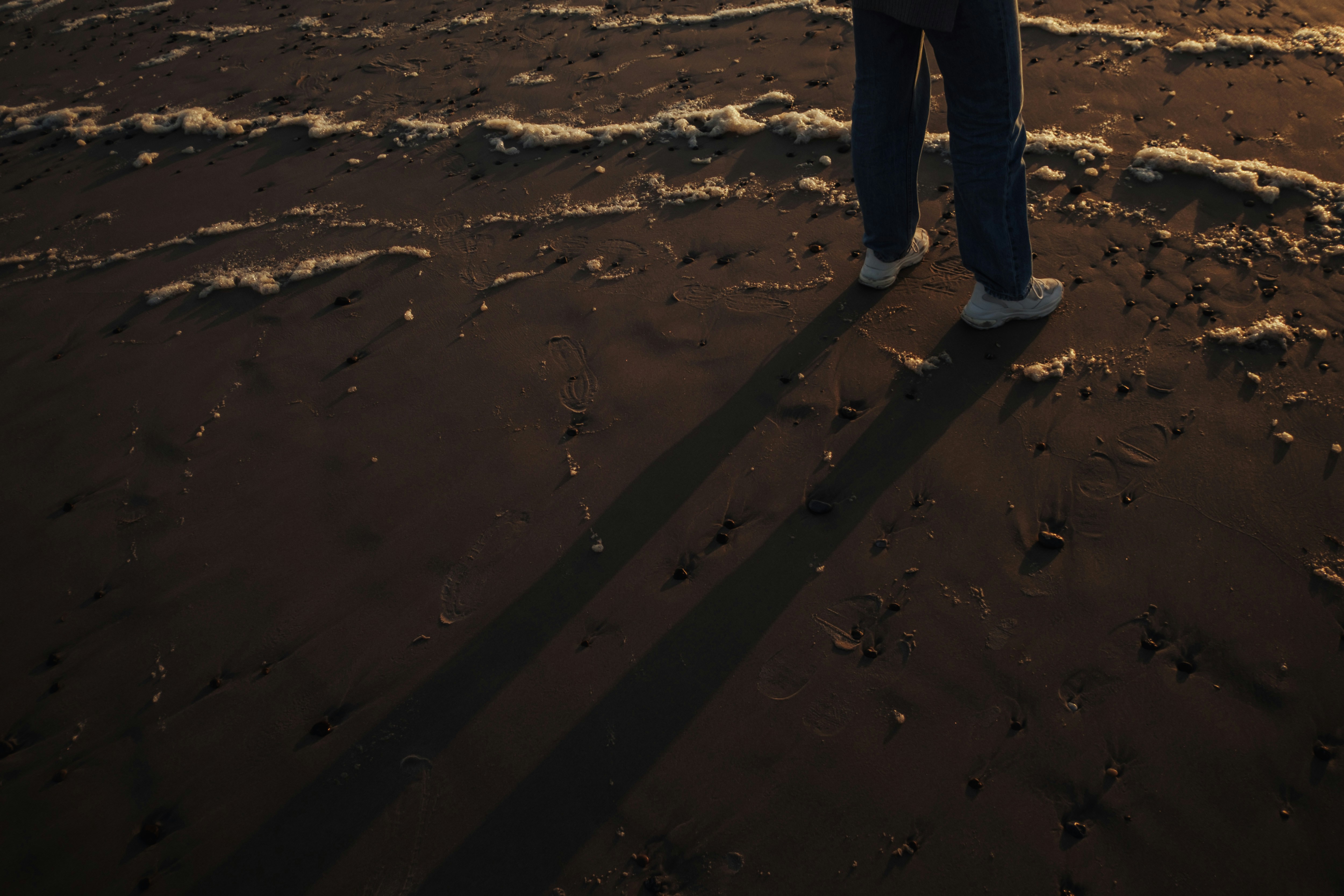 Person standing on the beach casts a long shadow.