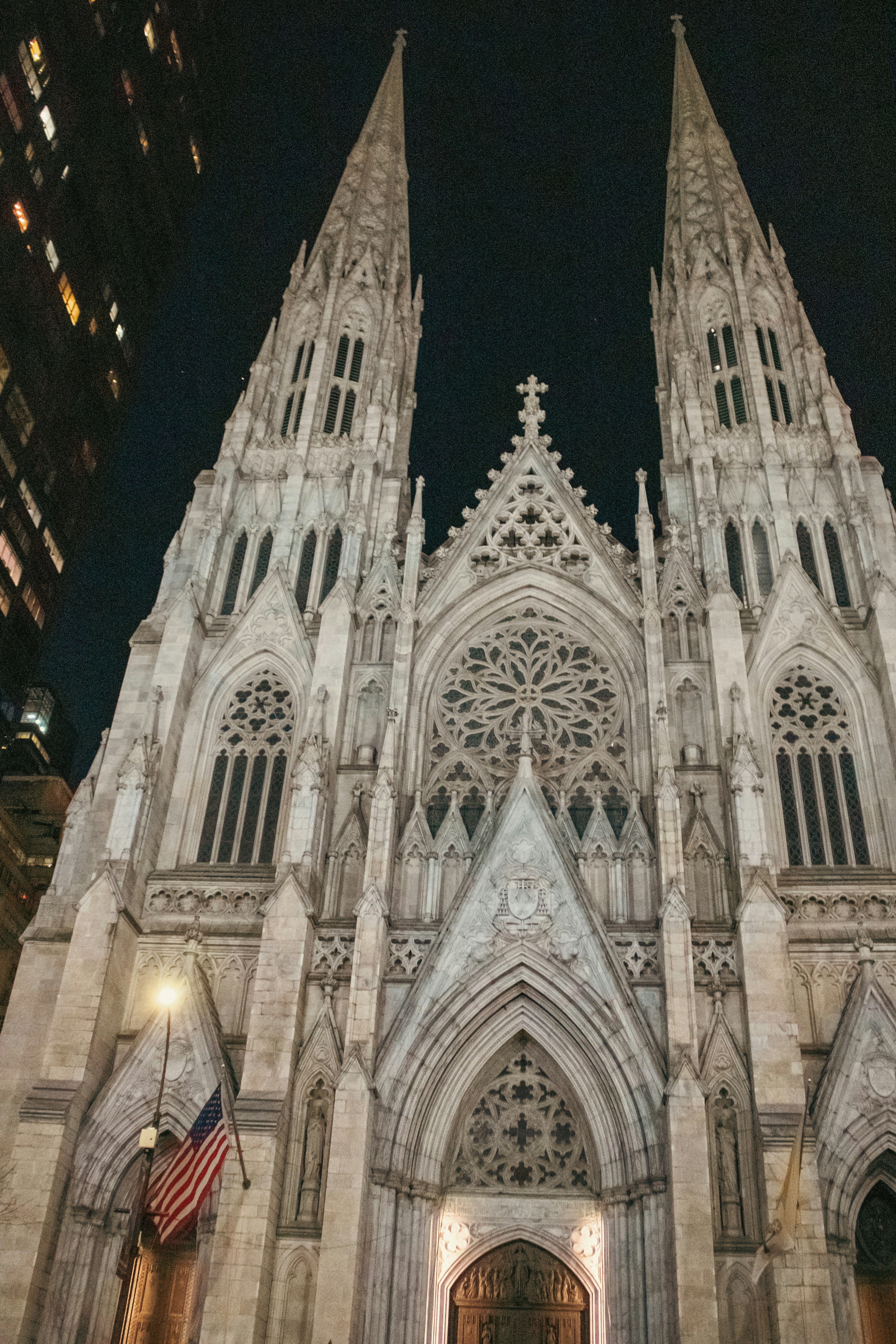 Intricate Gothic architecture of a cathedral illuminated at night, showcasing detailed stonework and towering spires.