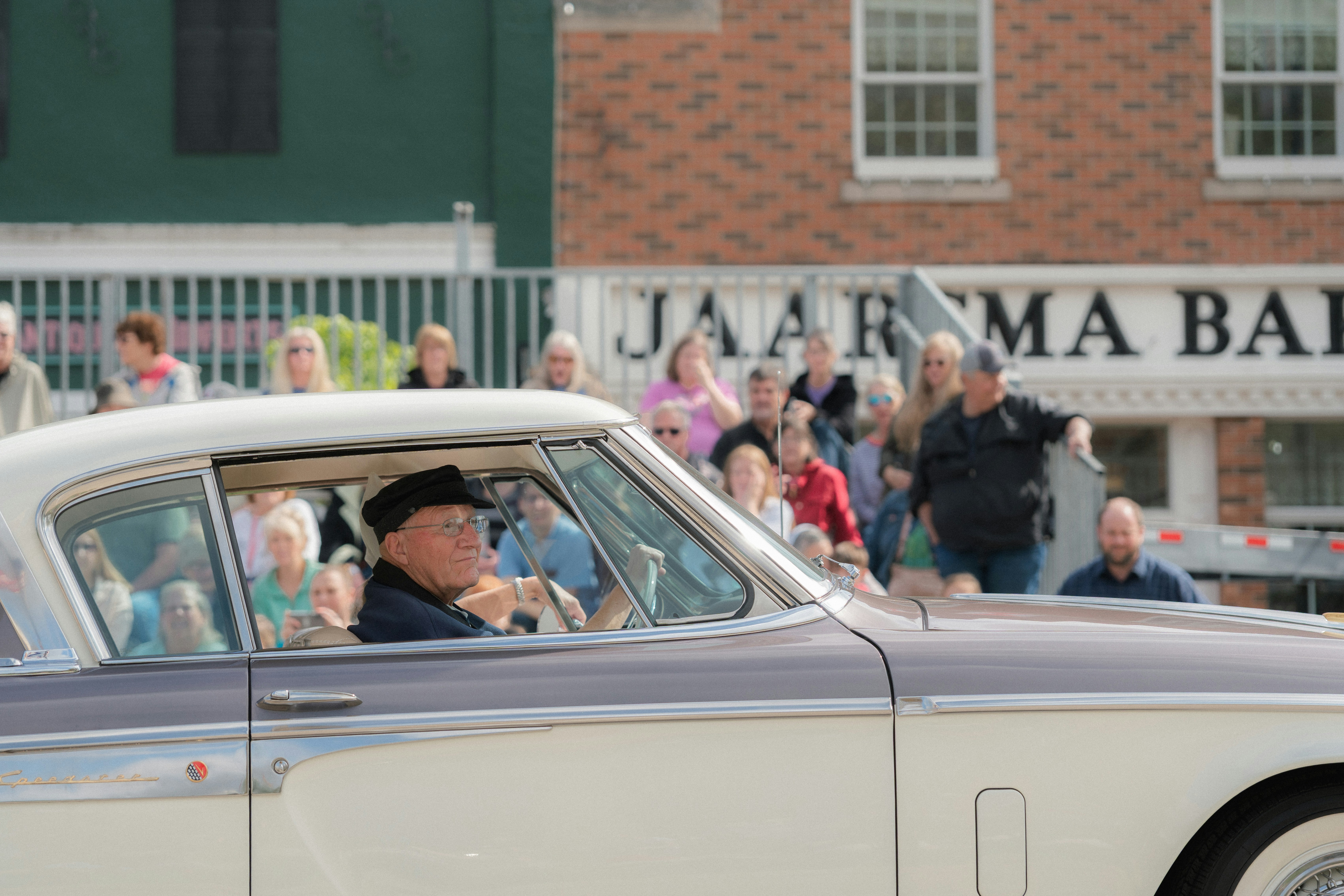 Pastel Parade: A 1950s Sedan Glides Past a Crowd Along a Brick storefront