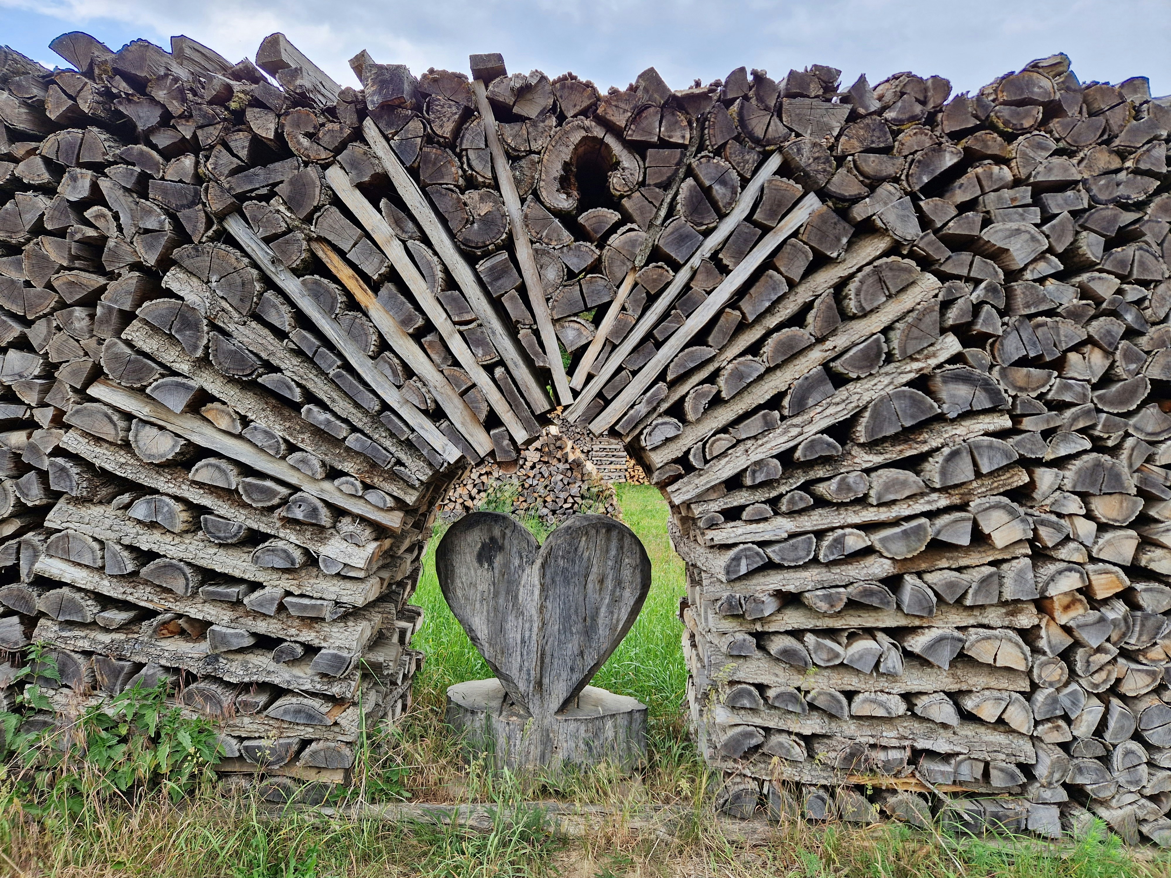 Wooden logs meticulously arranged to form an archway with a heart-shaped sculpture at the center, symbolizing love and nature's harmony.