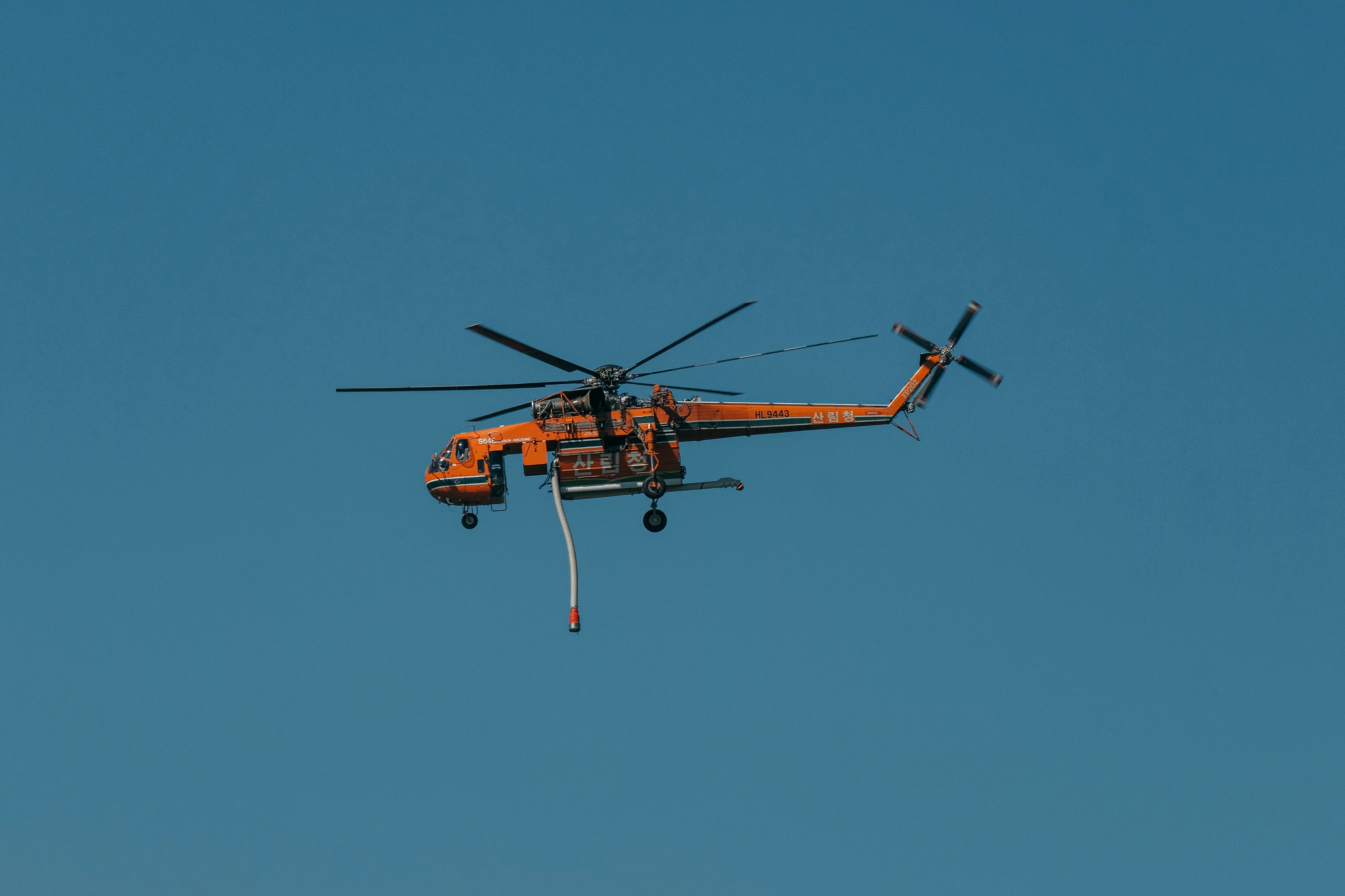 Orange Guardian in a Clear Sky: Firefighting Helicopter with Dropped Hose