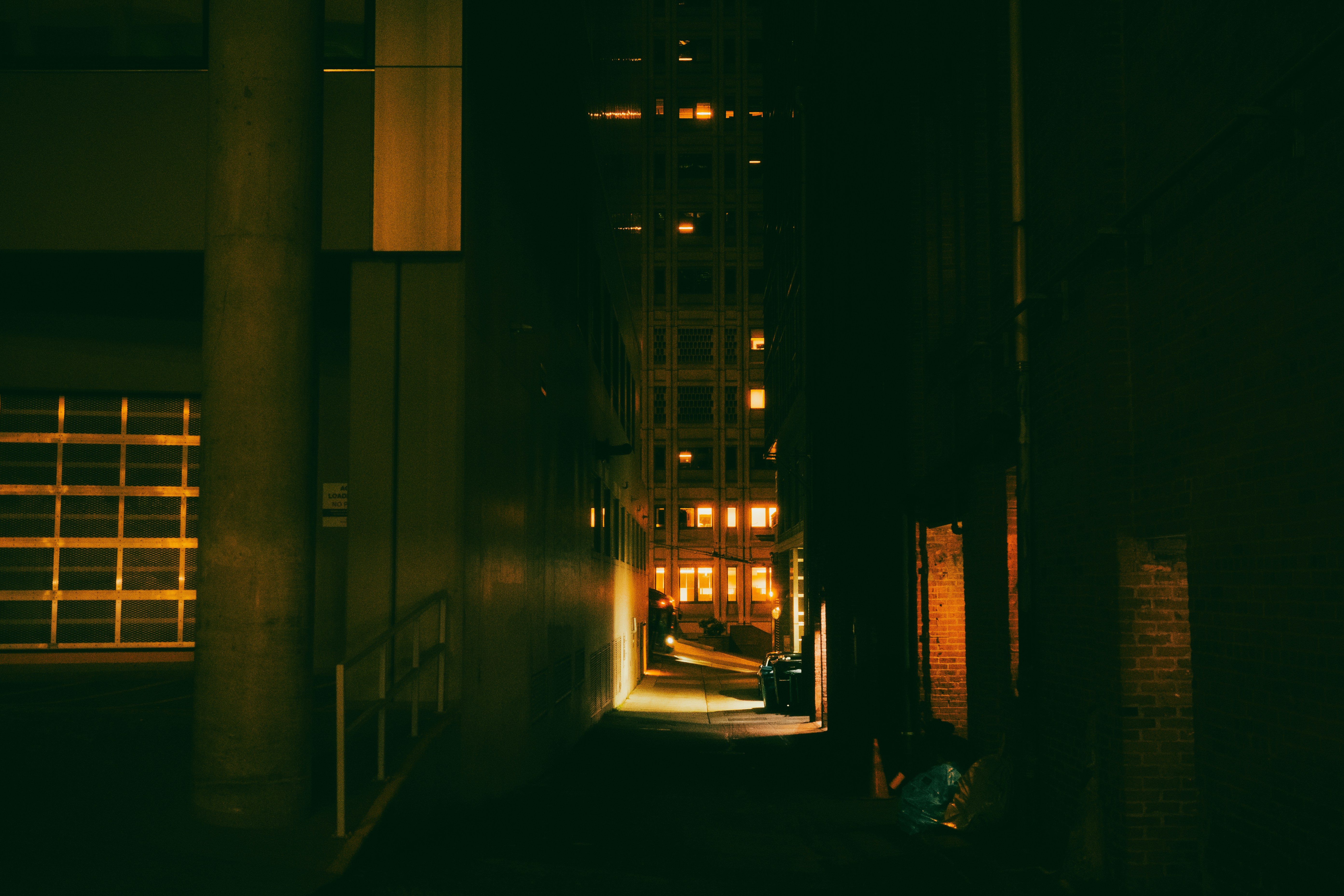 Dark alley leads to a brightly lit building.