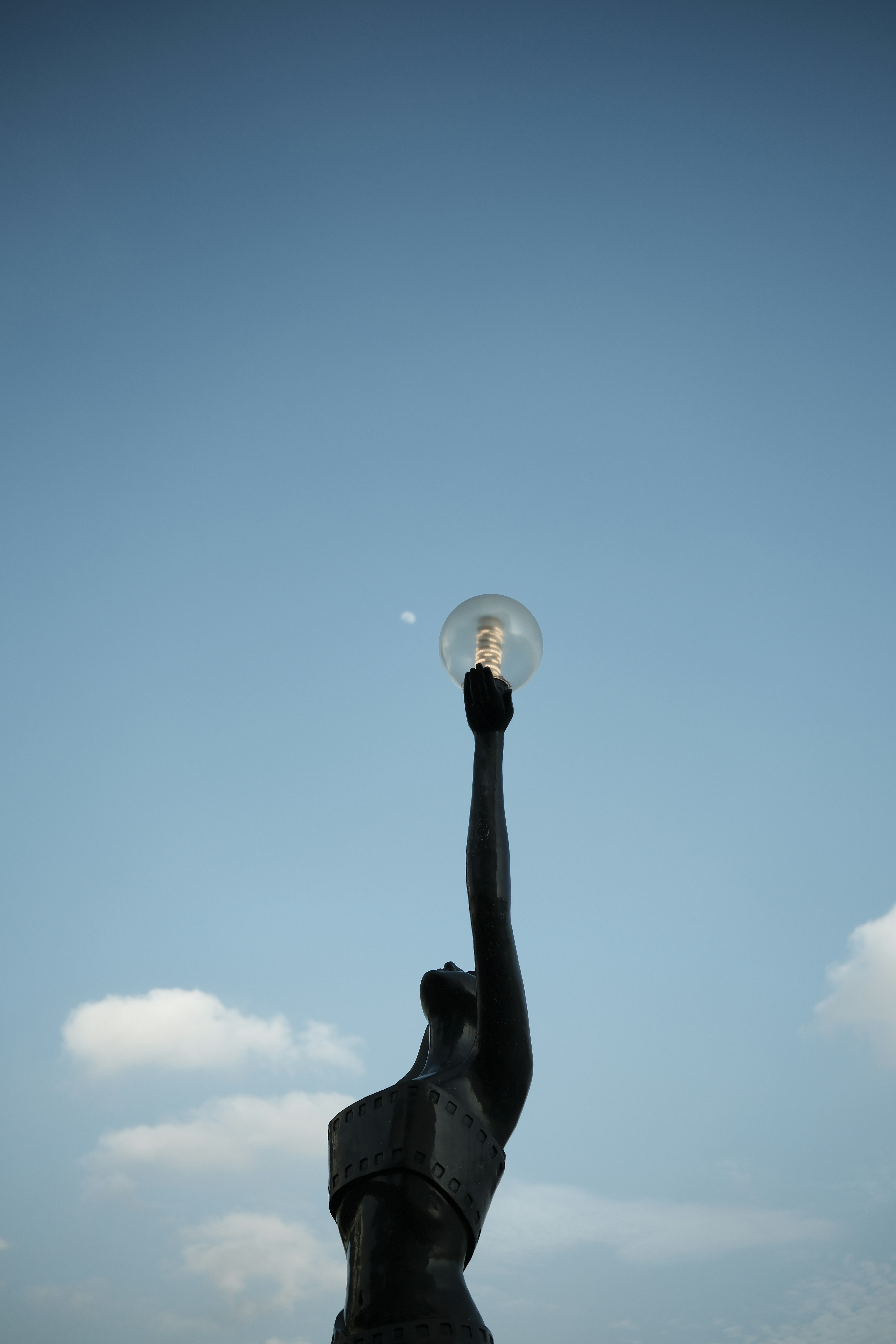 A striking sculpture of a figure holding a glowing orb against a clear sky, symbolizing inspiration and ambition.