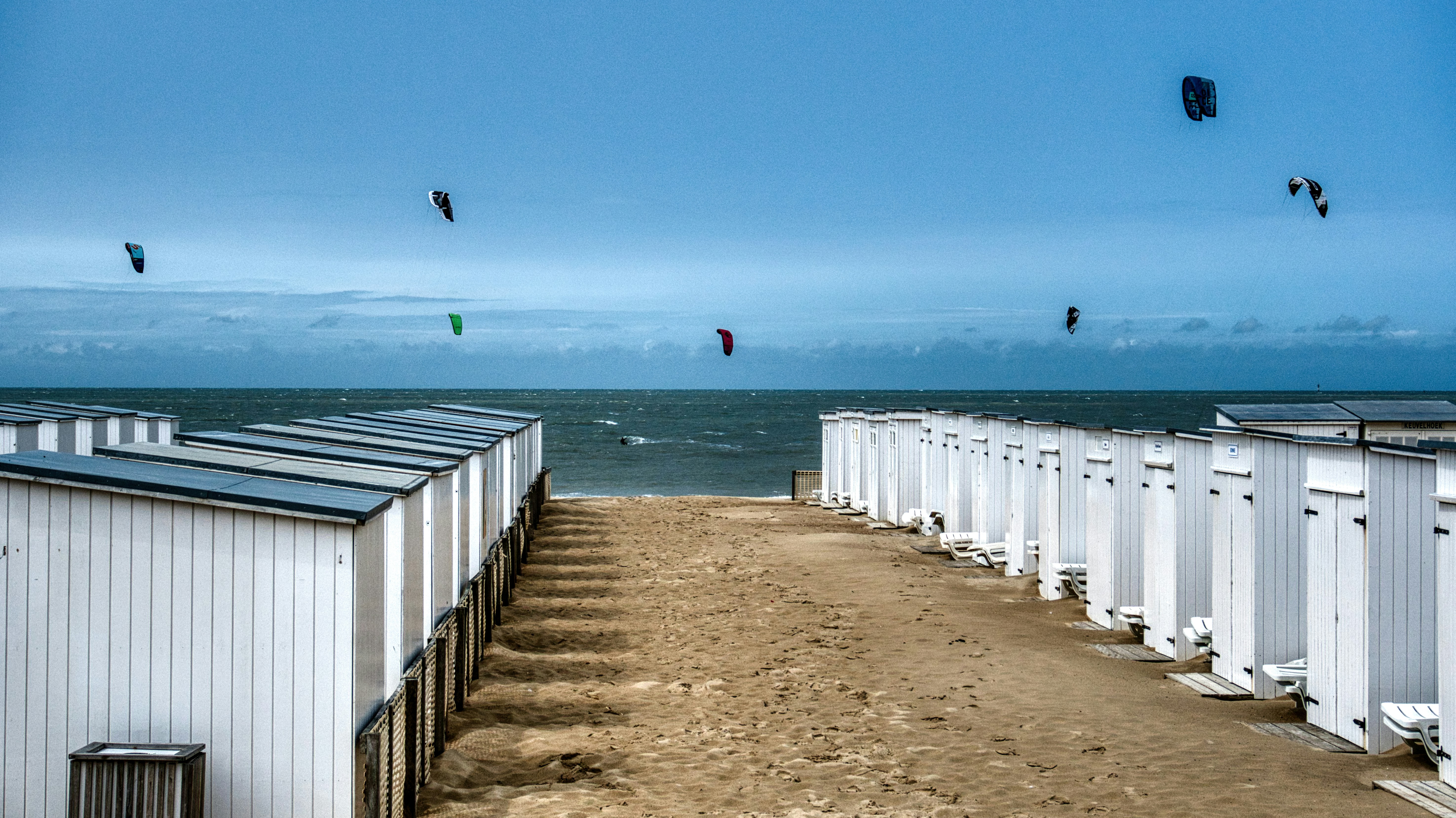 Seaside Corridor: White Cabins Framing a Kite-Dotted Horizon