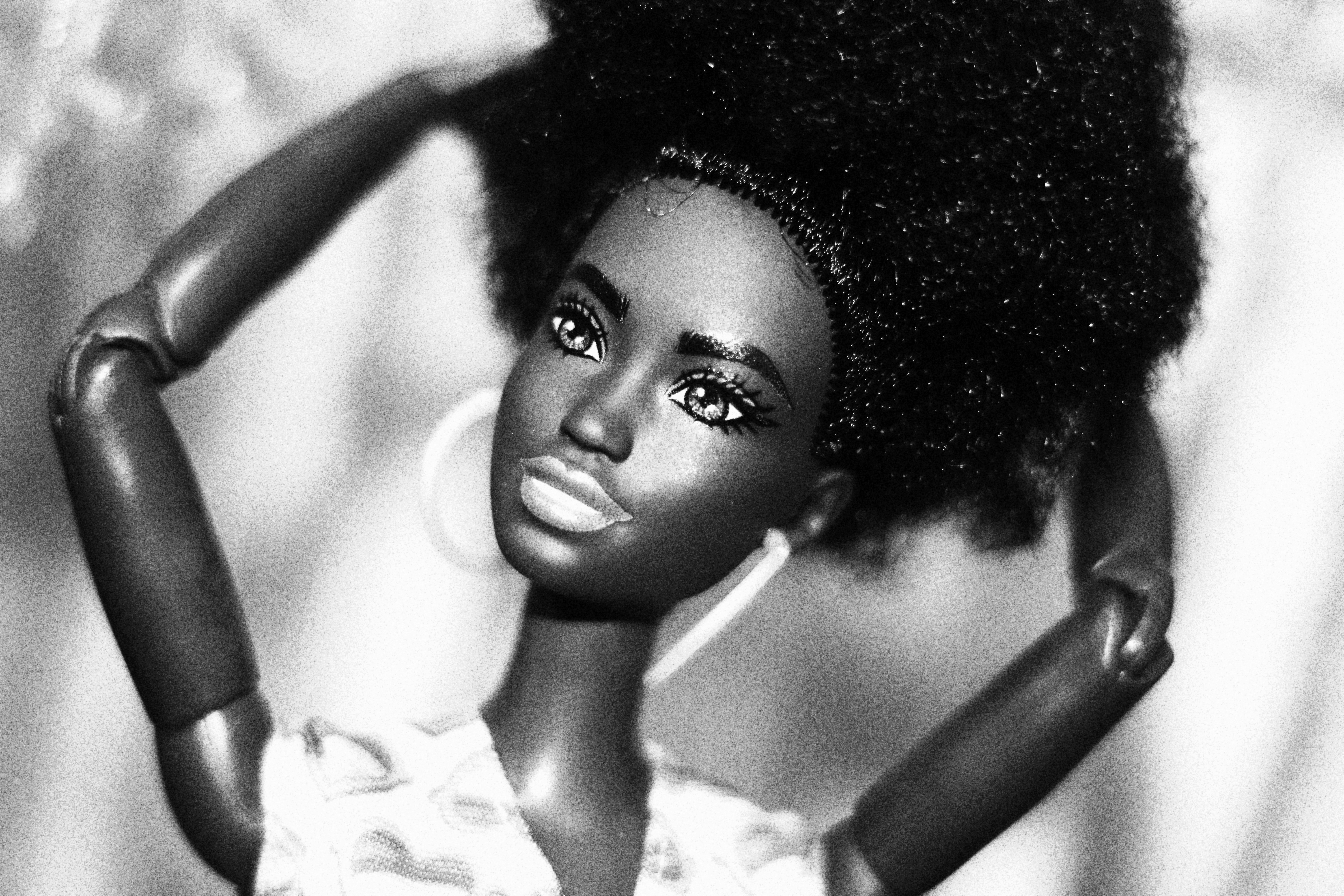 A close-up of a stylish doll with natural hair, showcasing intricate facial features and accessories. The monochrome effect adds a timeless quality.