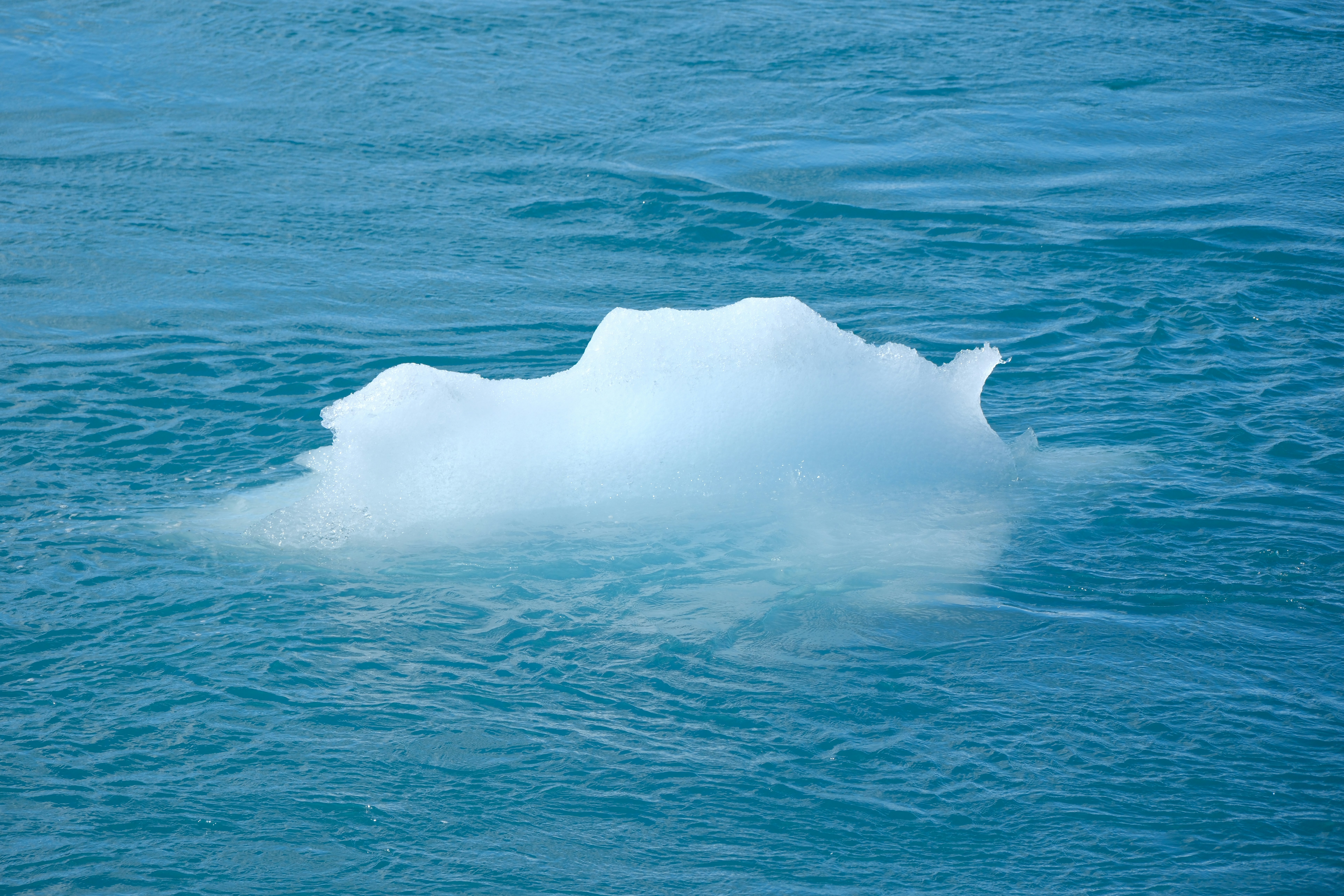 Lonely iceberg floating on tranquil blue waters, glistening under the sun's rays.