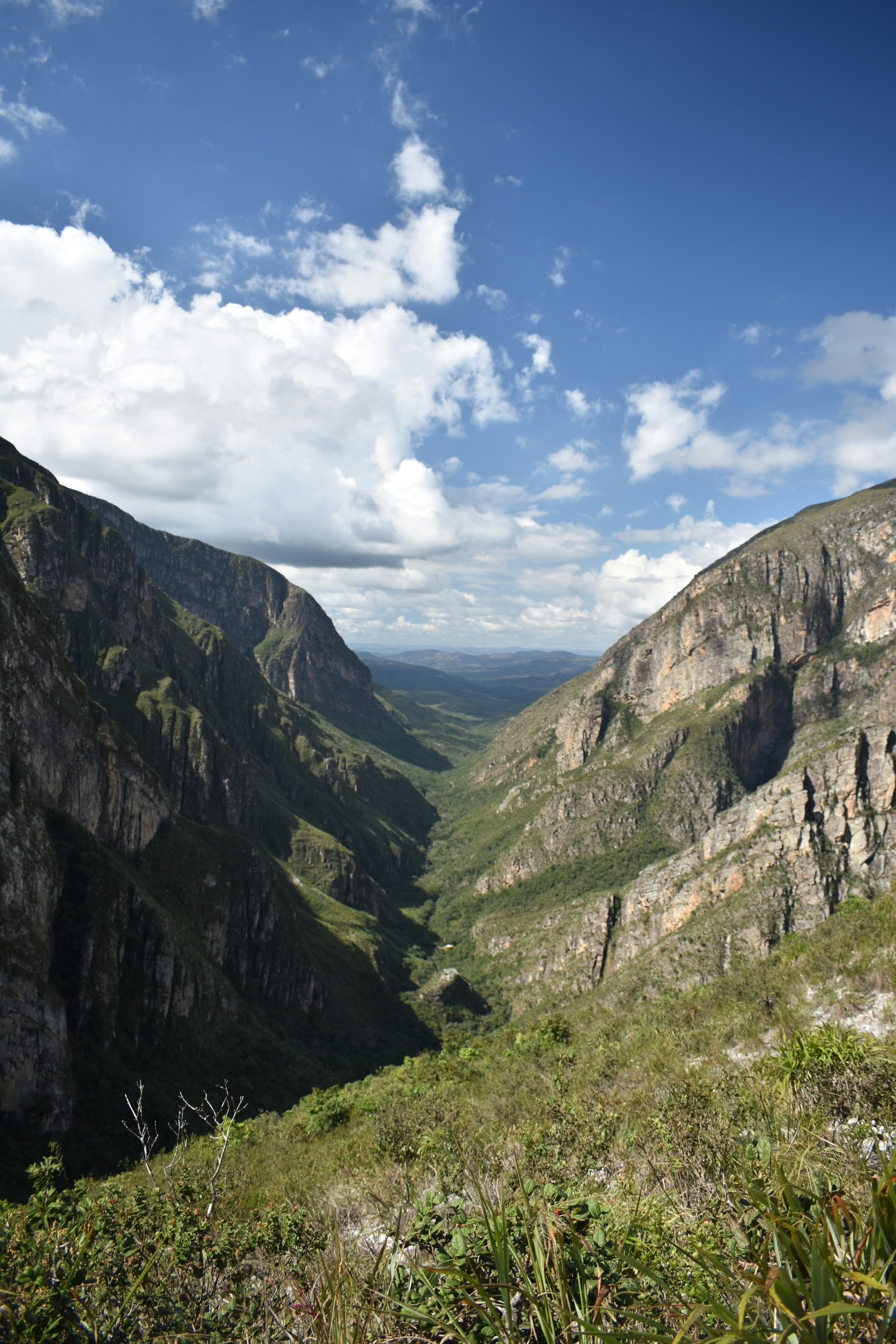 Expansive view of a lush valley surrounded by towering cliffs under a partly cloudy sky. The scene captures the rugged beauty of the landscape.